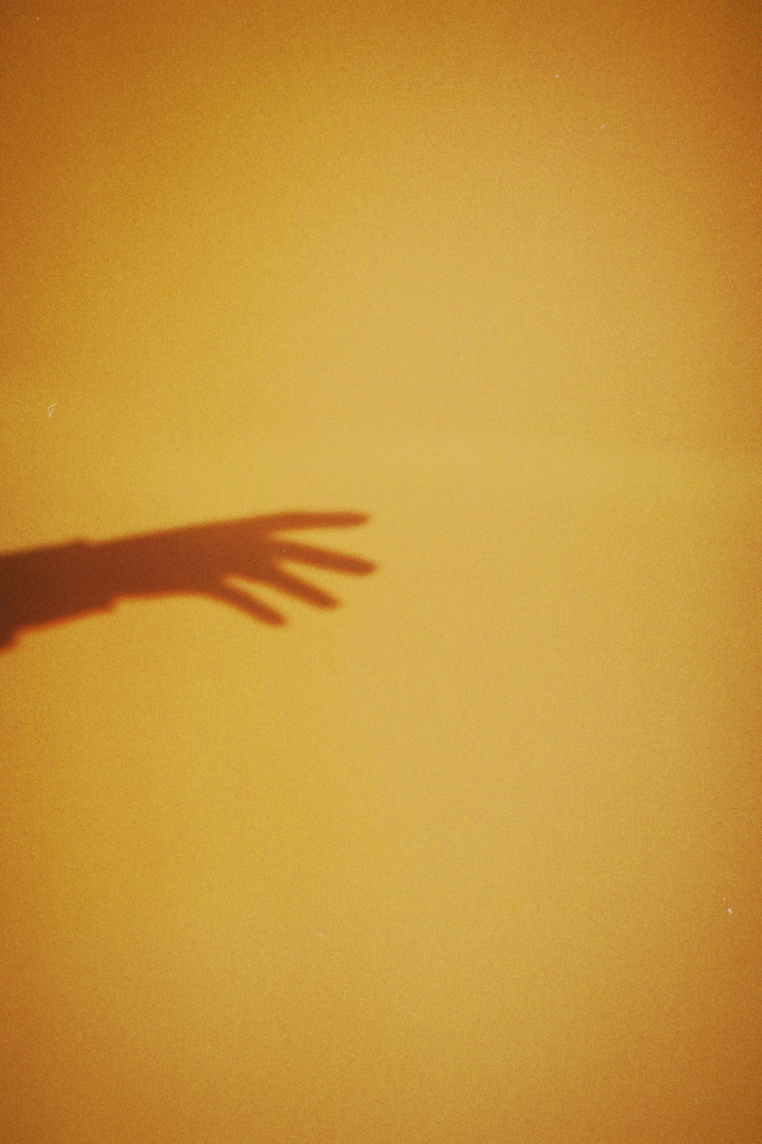 Dramatic Hand Shadow on Vibrant Yellow Wall · Free Stock Photo