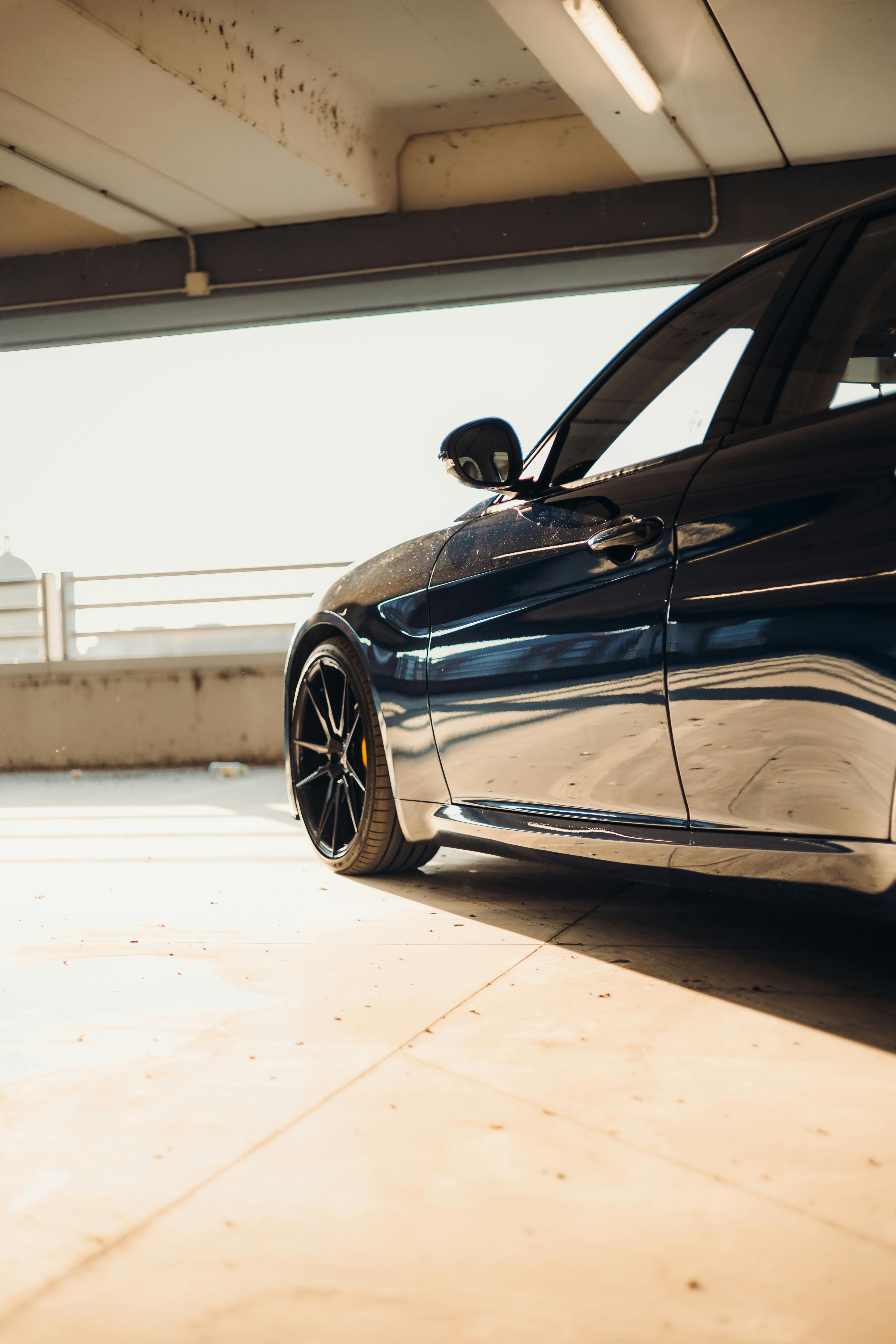Sleek Black Car in Sunlit Parking Garage · Free Stock Photo