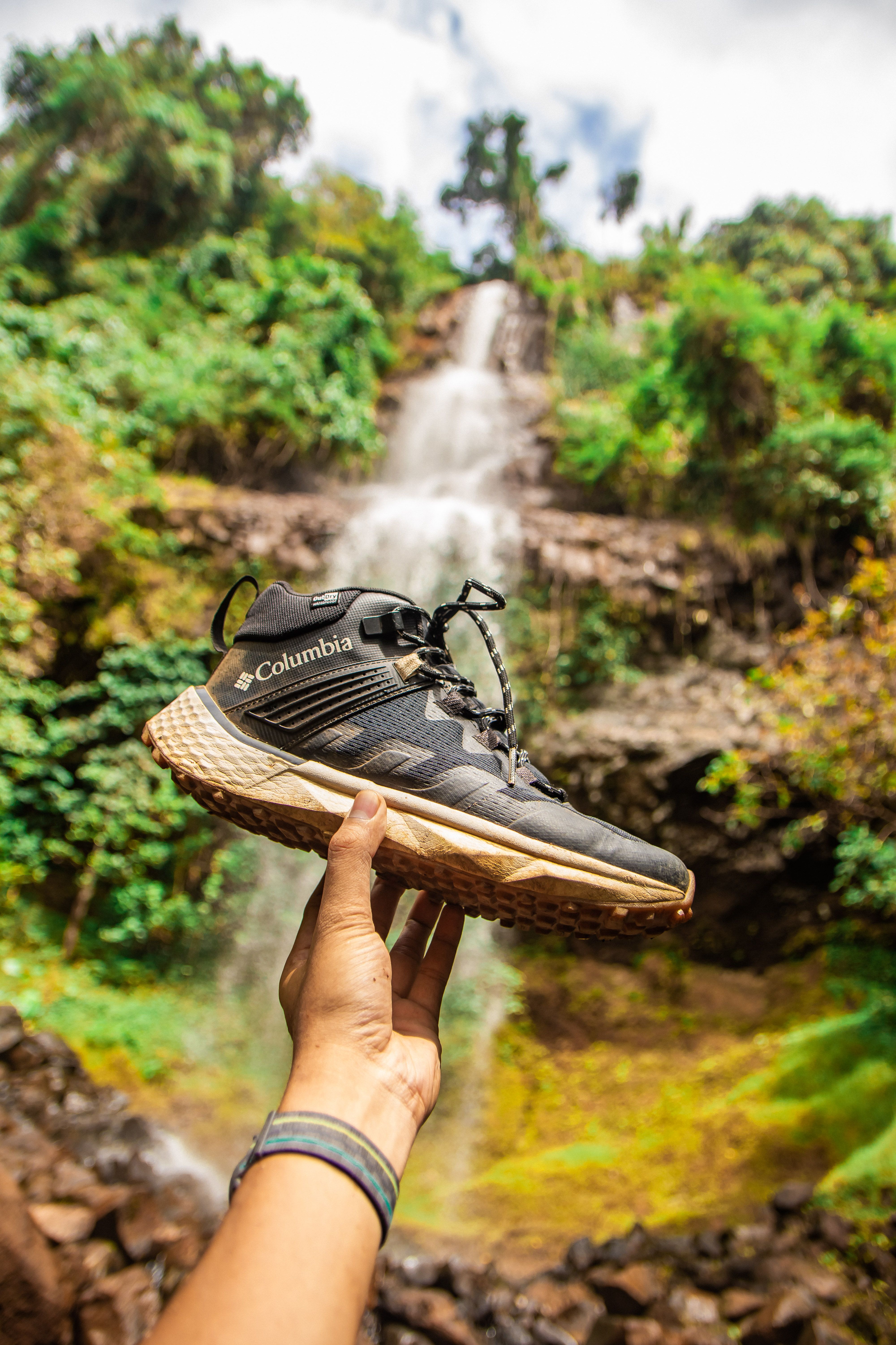 Trekking Shoe Held in Front of Đắk Nông Waterfall · Free Stock Photo