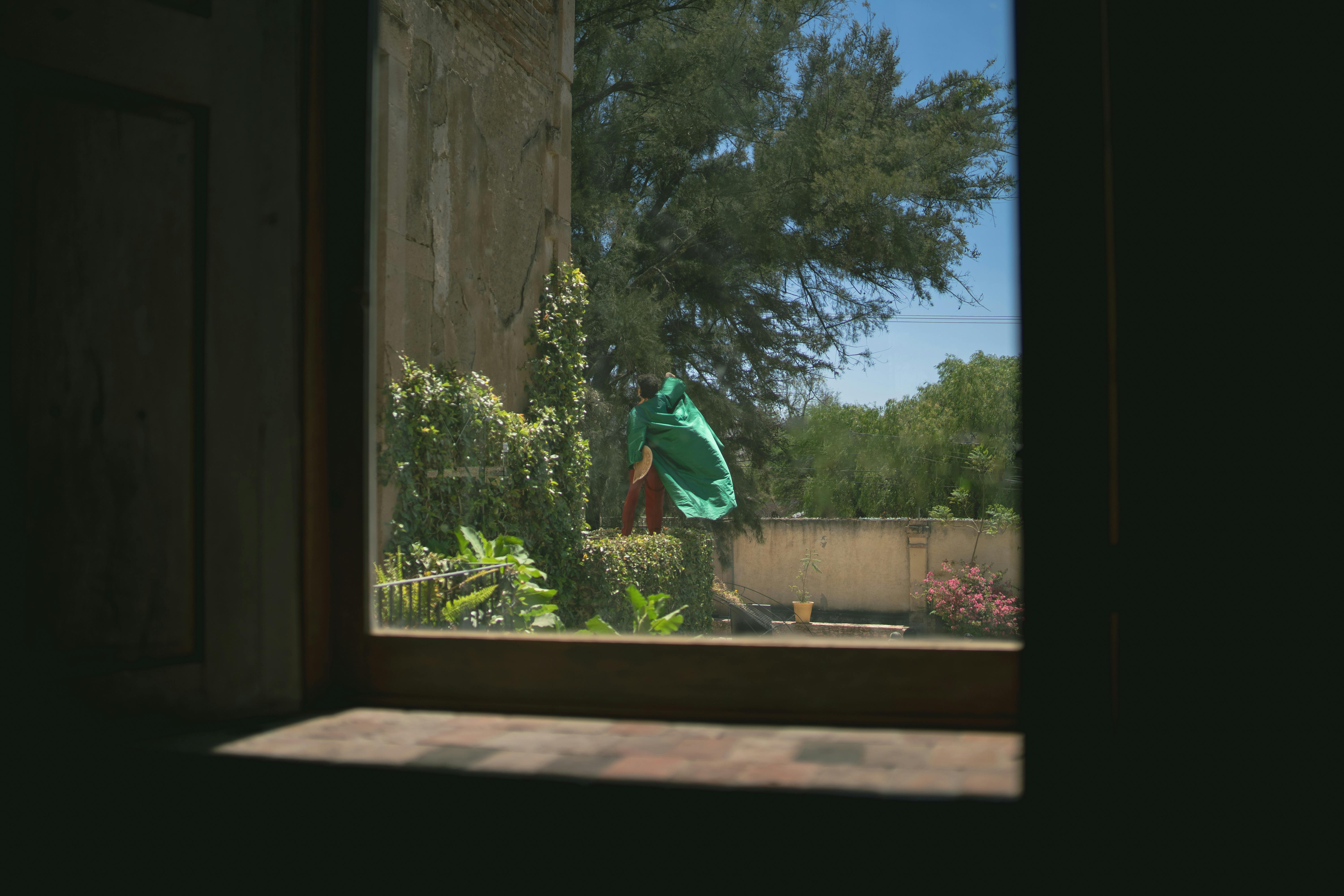 View Through Window of Green-Clad Figure Outdoors · Free Stock Photo