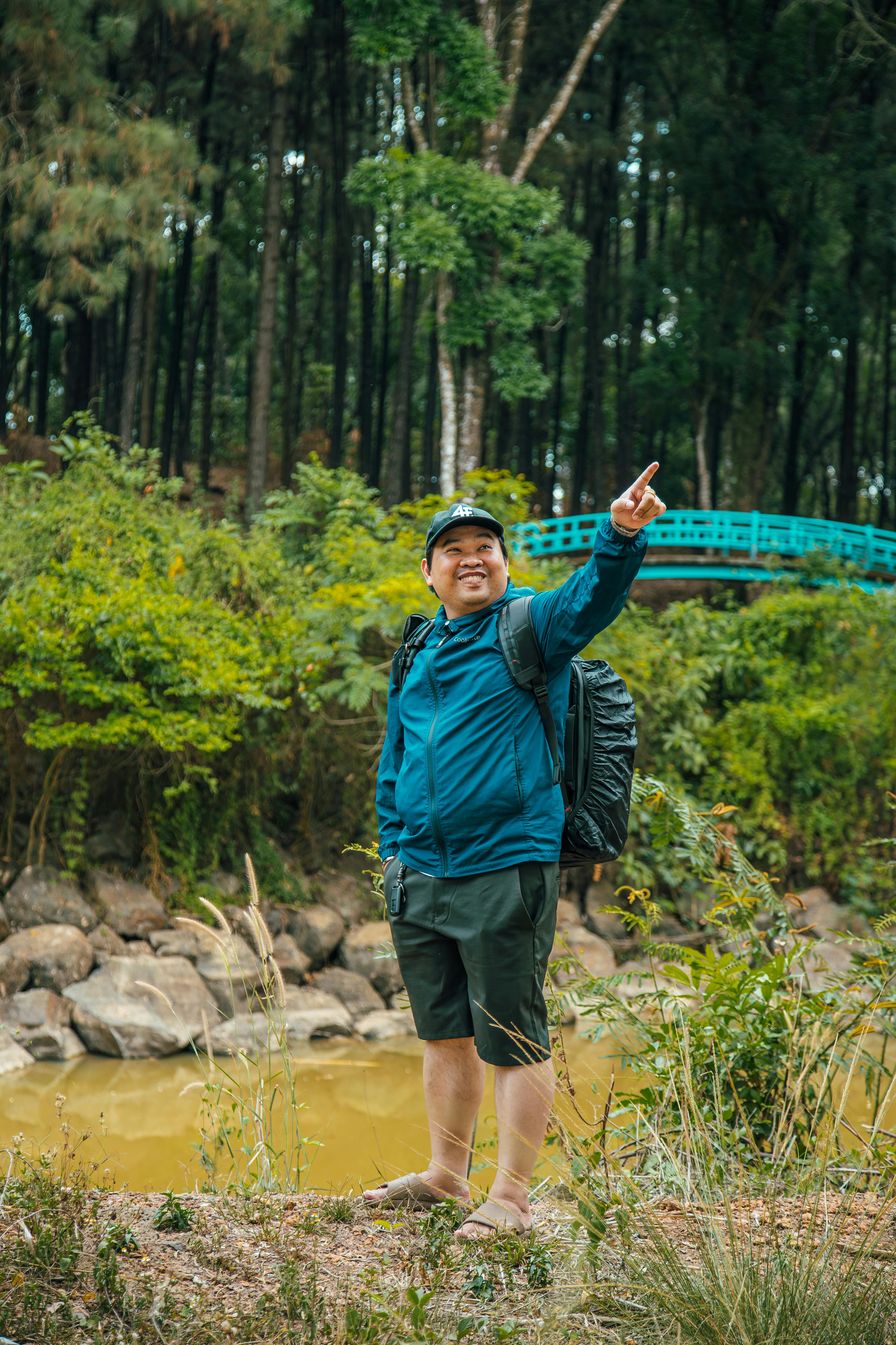 Smiling Hiker Points in Forest with Backpack · Free Stock Photo