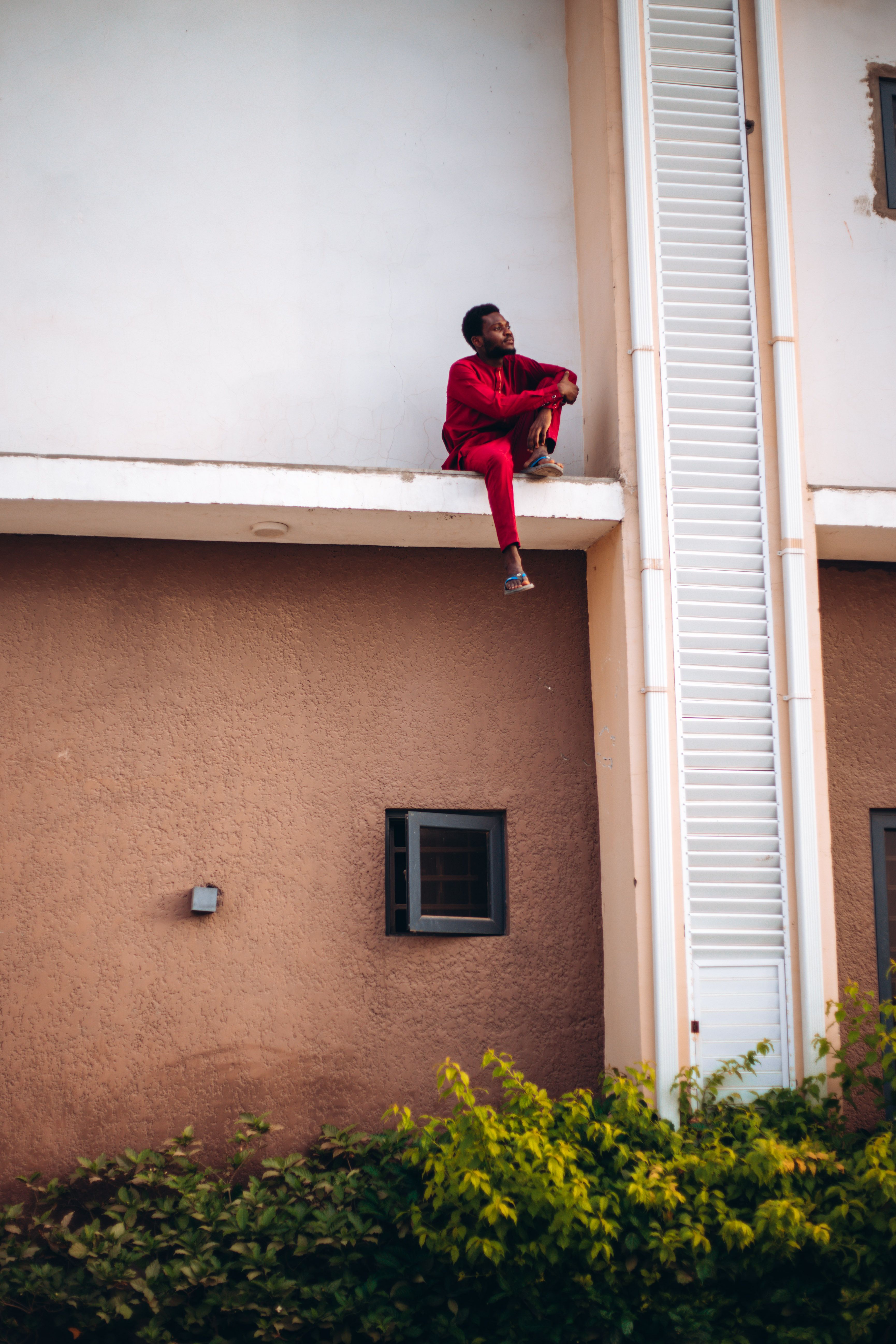 Man Sitting High on Building Ledge in Urban Setting · Free Stock Photo