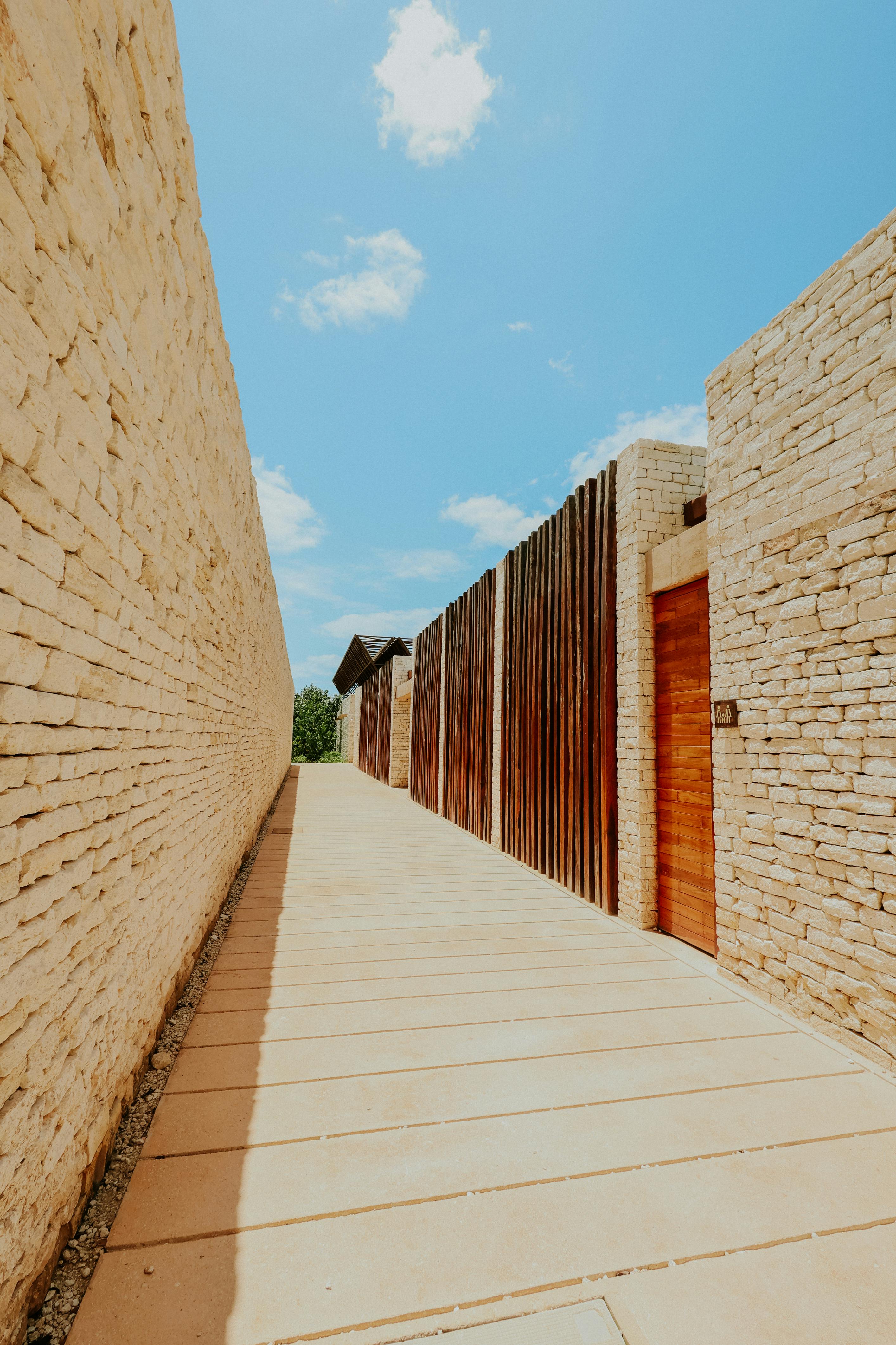 Sunny Pathway Along Stone and Wood Walls · Free Stock Photo