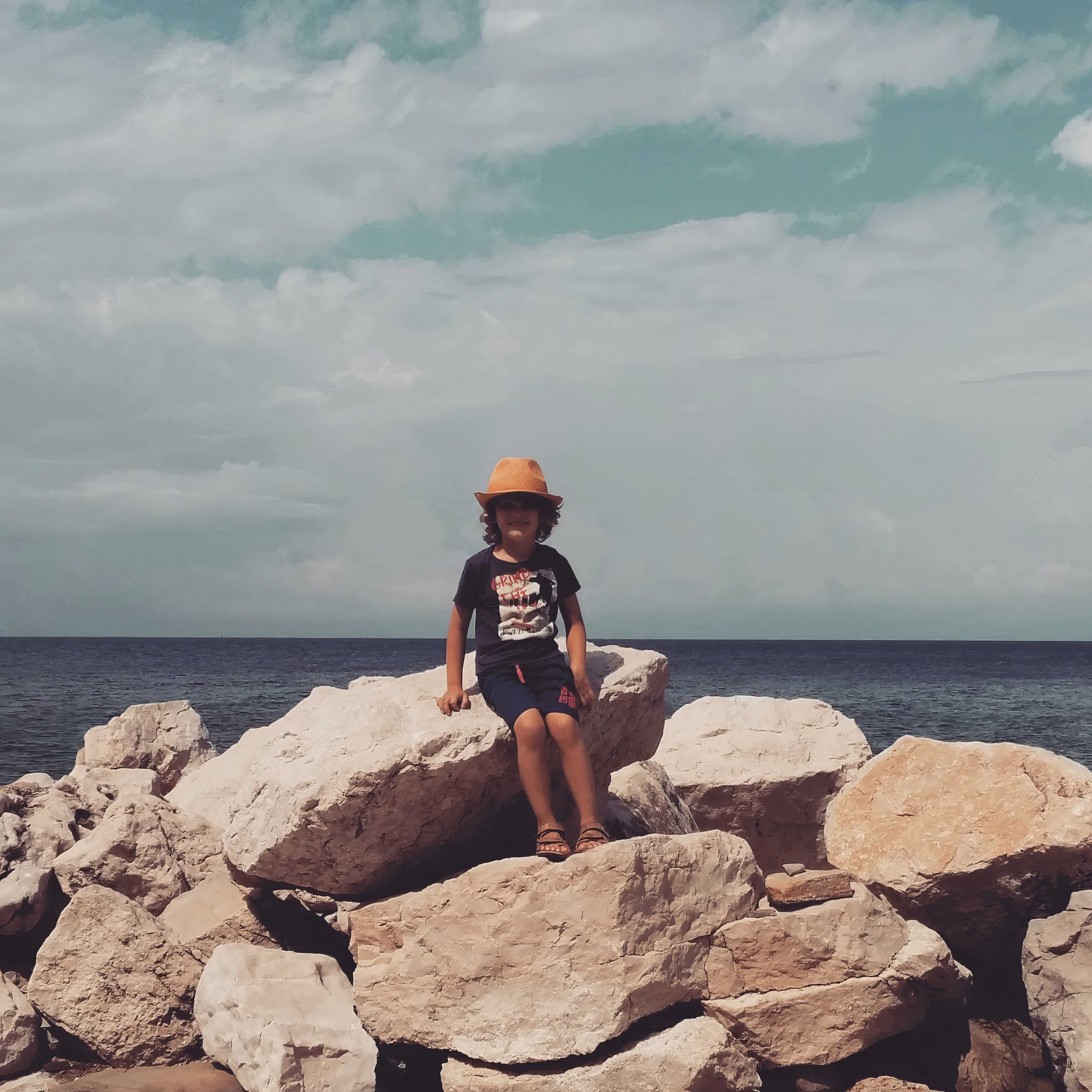 Child in Yellow Hat on Coastal Rocks in Summer · Free Stock Photo