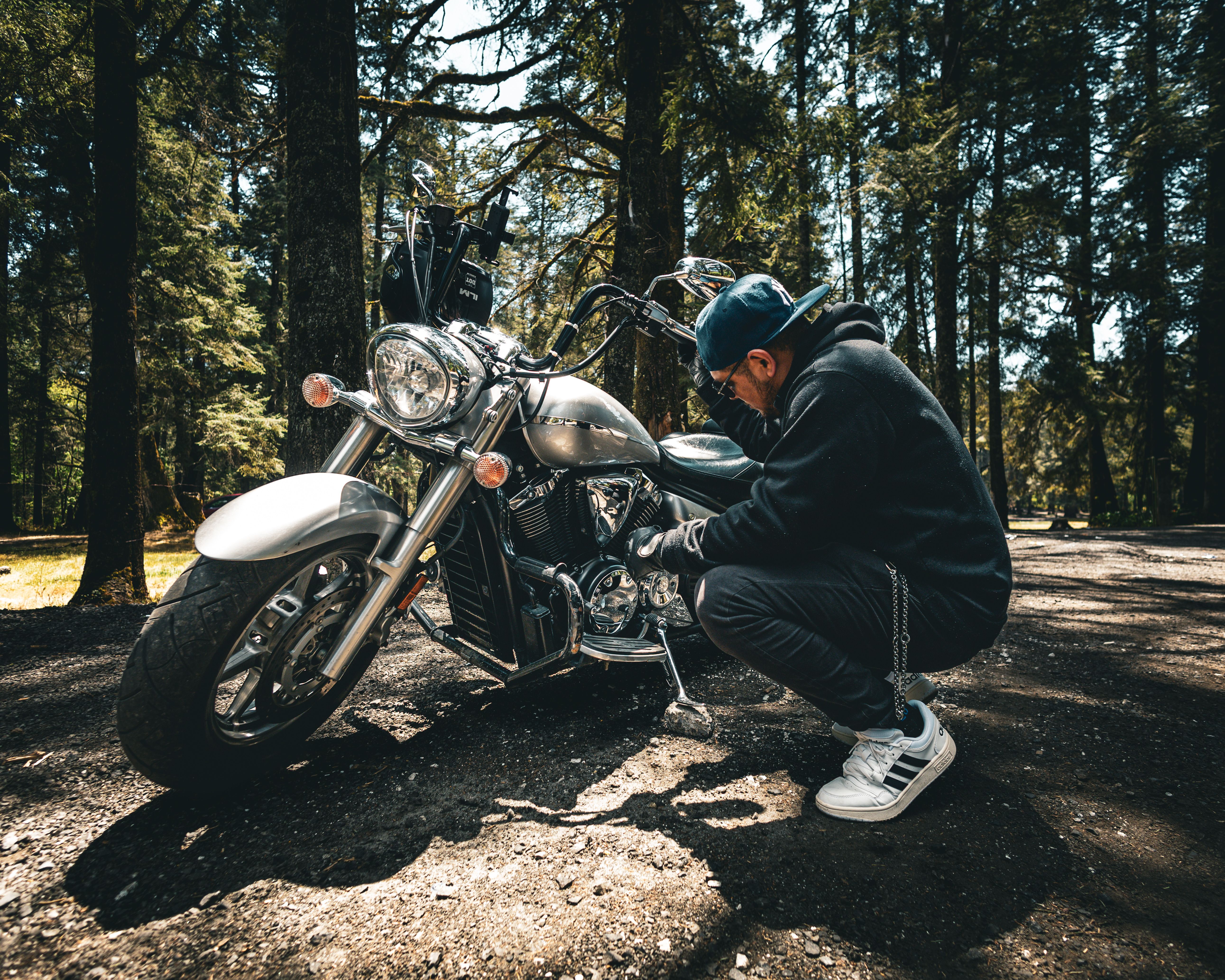 Man Inspecting Motorcycle in Forest Setting · Free Stock Photo