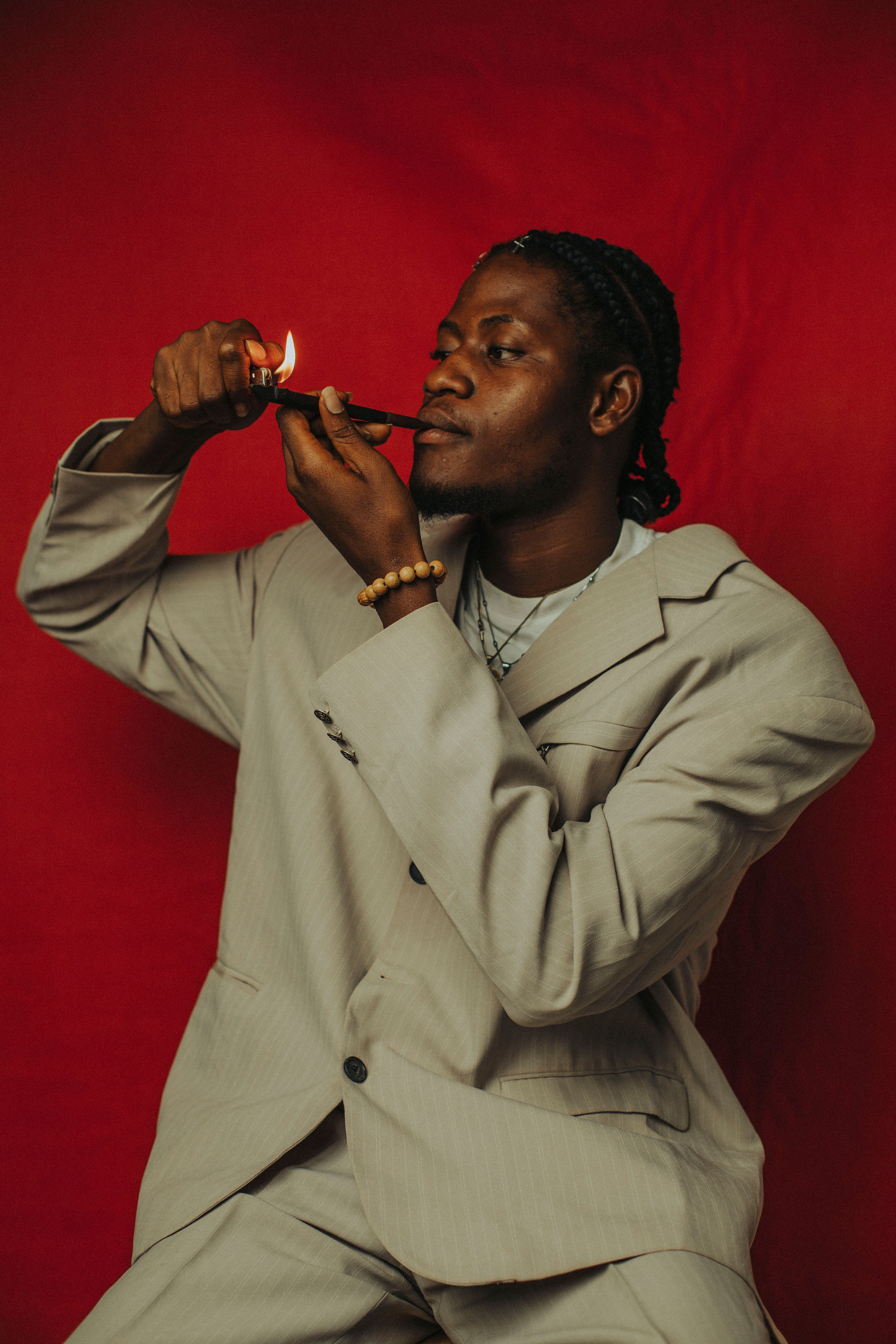 Man in Beige Suit Lighting a Pipe Against Red Background · Free Stock Photo