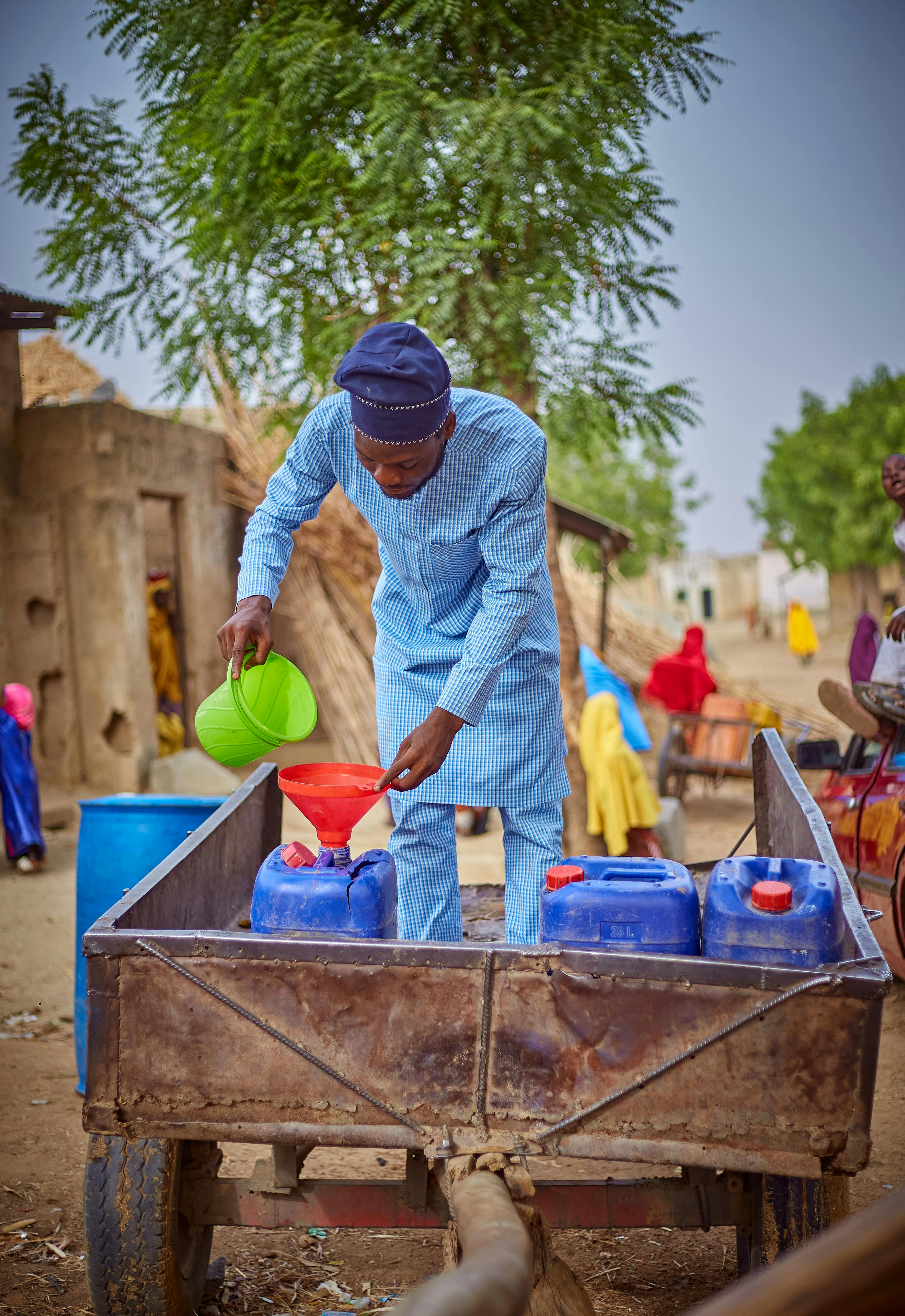 Man Transferring Liquid into Blue Containers in Village · Free Stock Photo