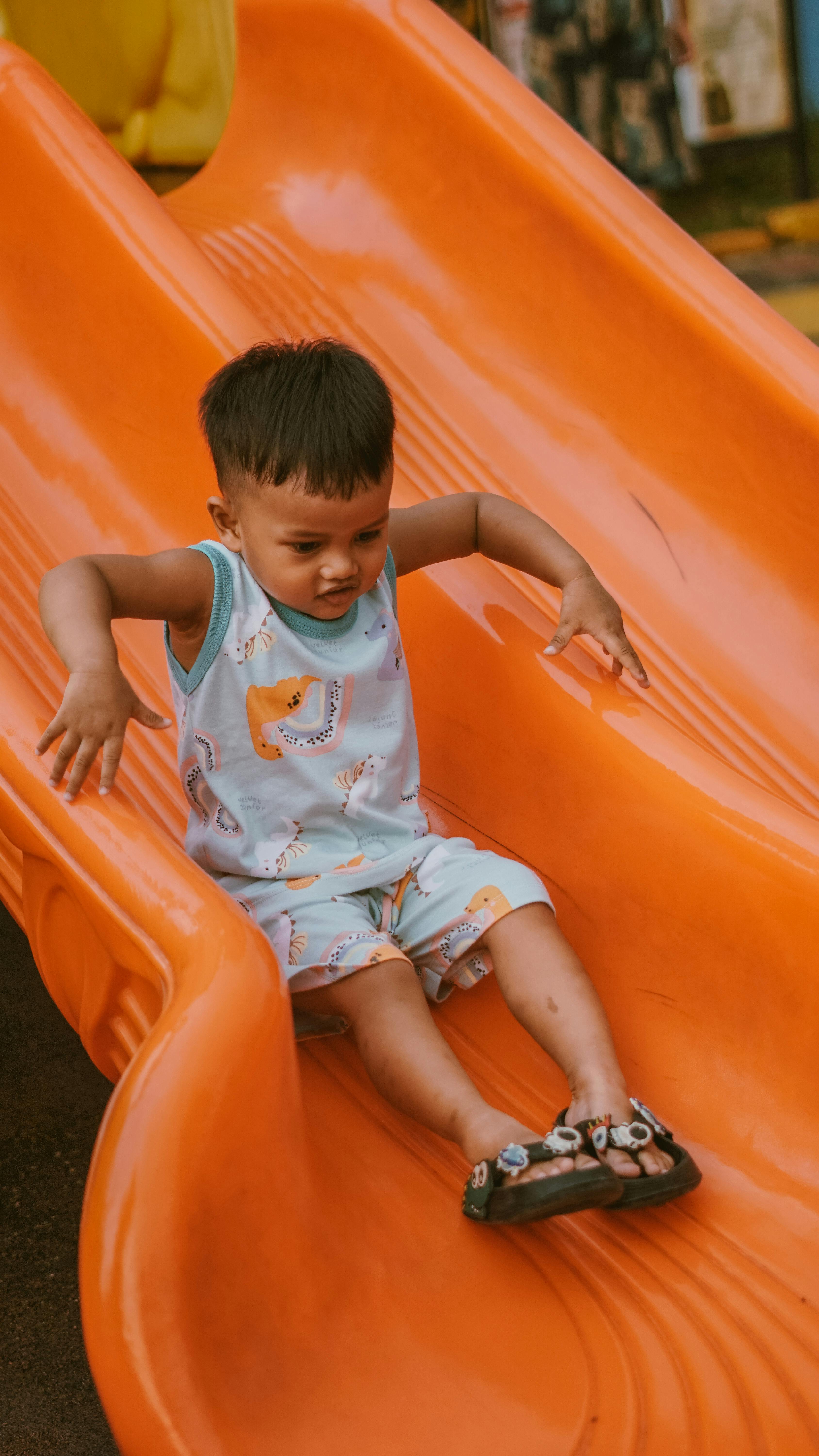 Joyful Child Sliding in Vibrant Orange Playground · Free Stock Photo