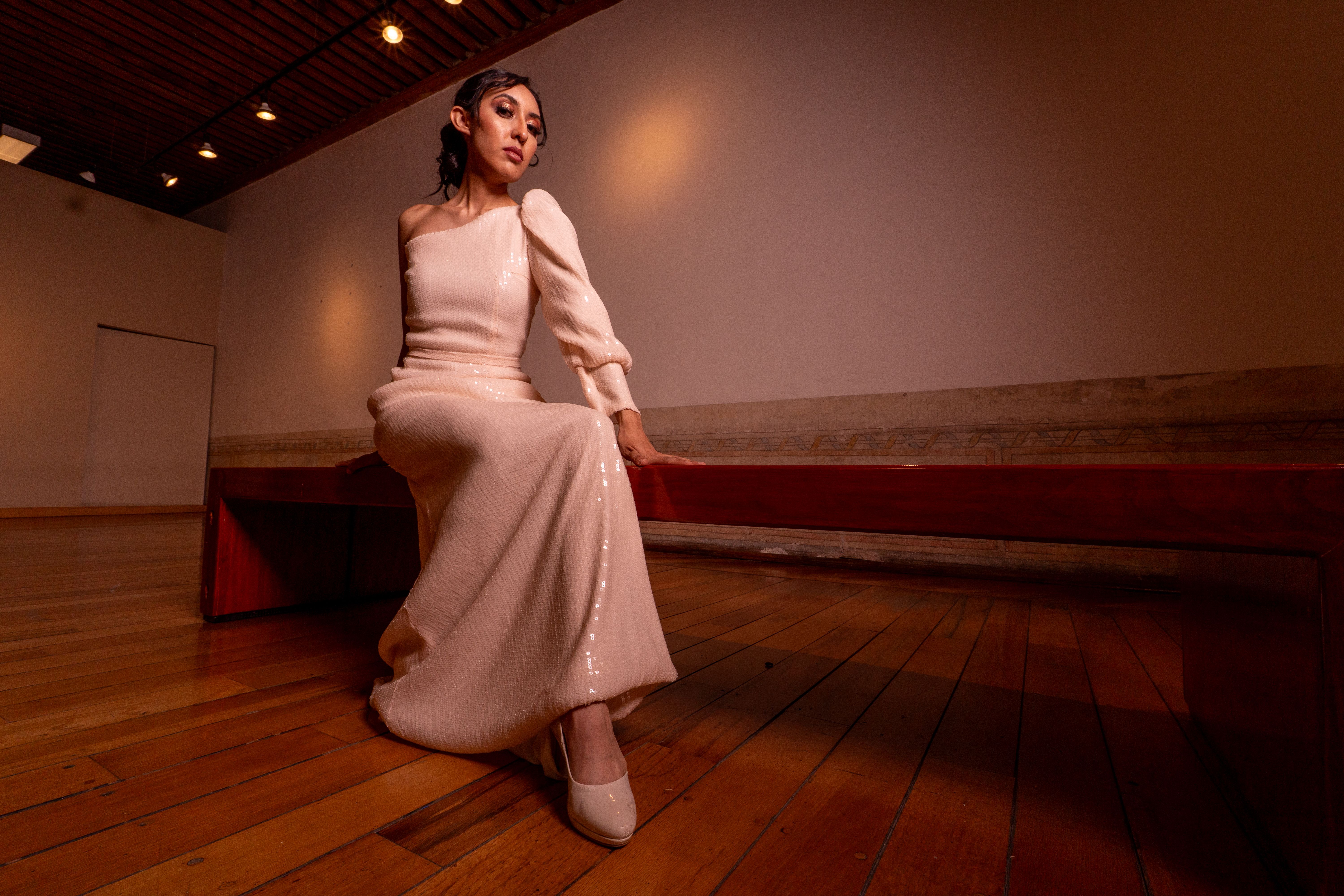 Elegant Woman in Ivory Dress Sitting on Bench in Gallery · Free Stock Photo
