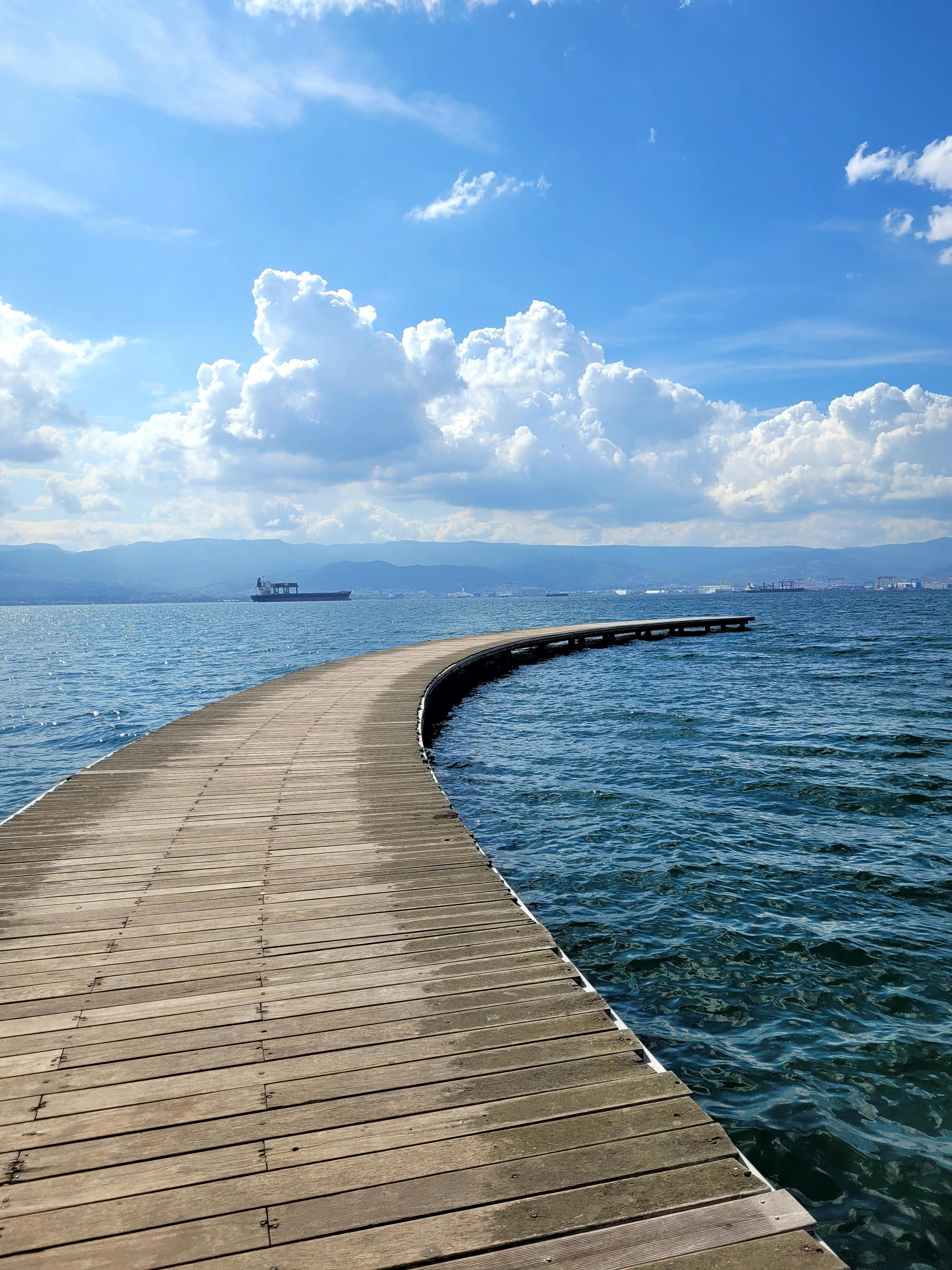 Curved Wooden Pier Extending Over Ocean Horizon · Free Stock Photo