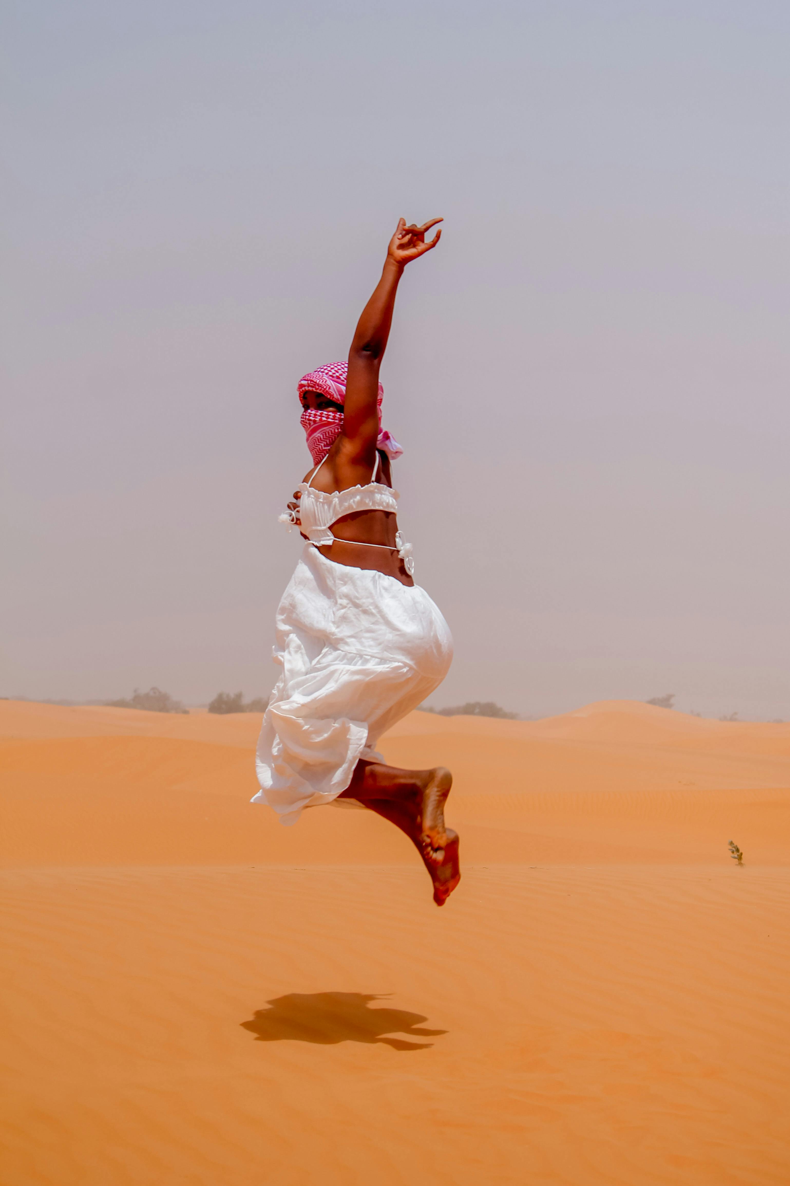 Jumping Figure in Desert Wearing Traditional Scarf · Free Stock Photo