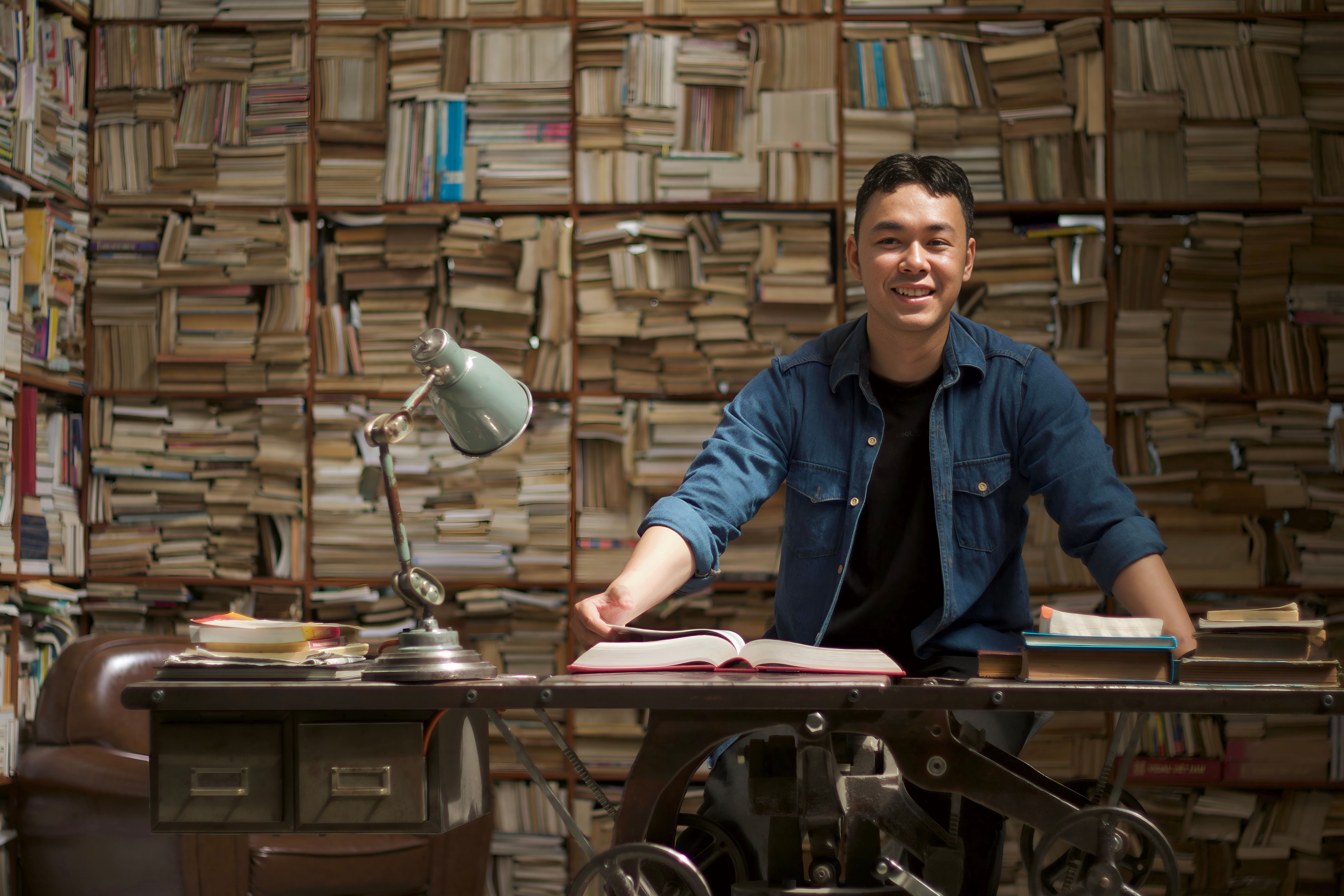 Man in Library Surrounded by Stacked Books · Free Stock Photo