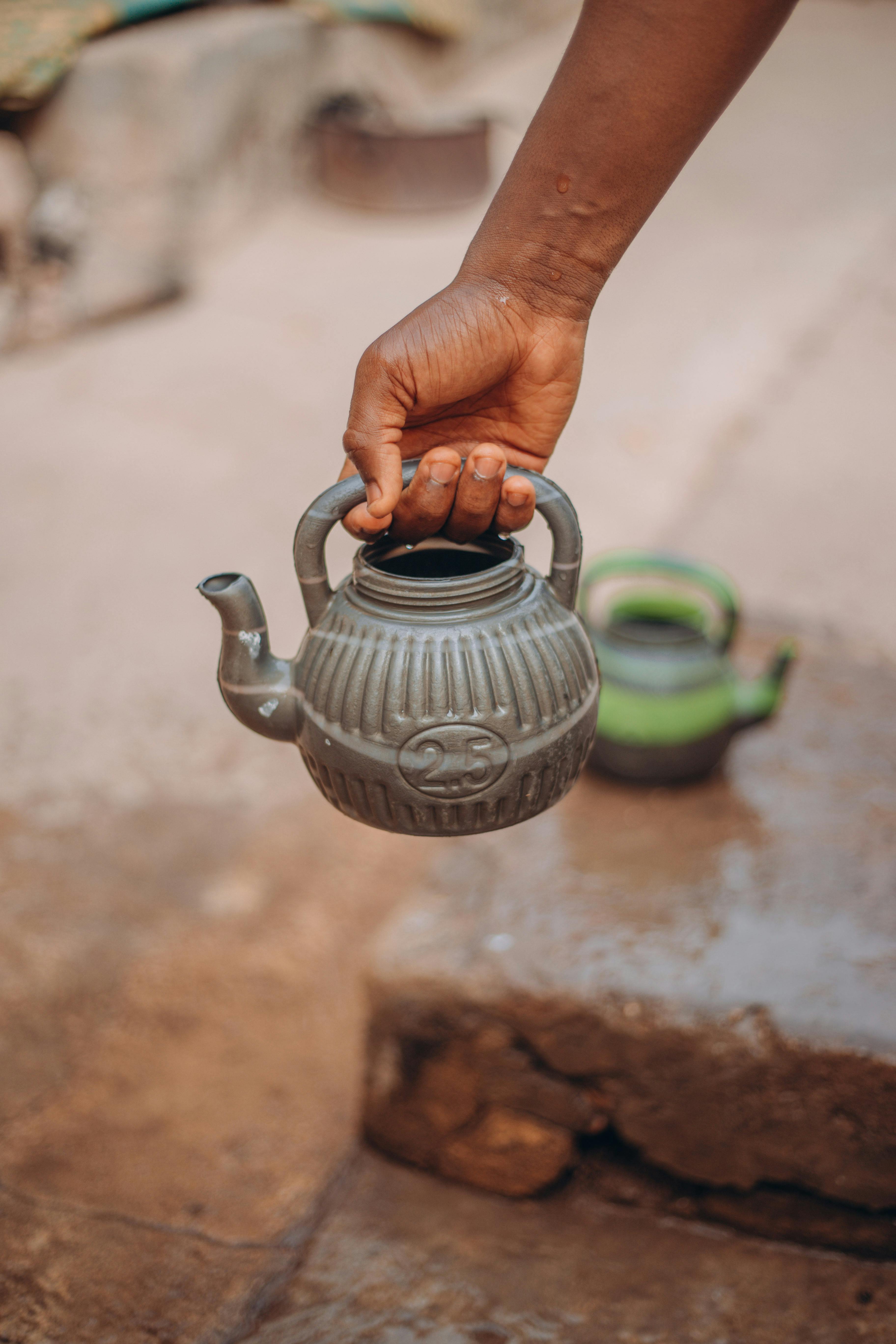 African Hand Holding Rustic Teapot in Outdoor Setting · Free Stock Photo