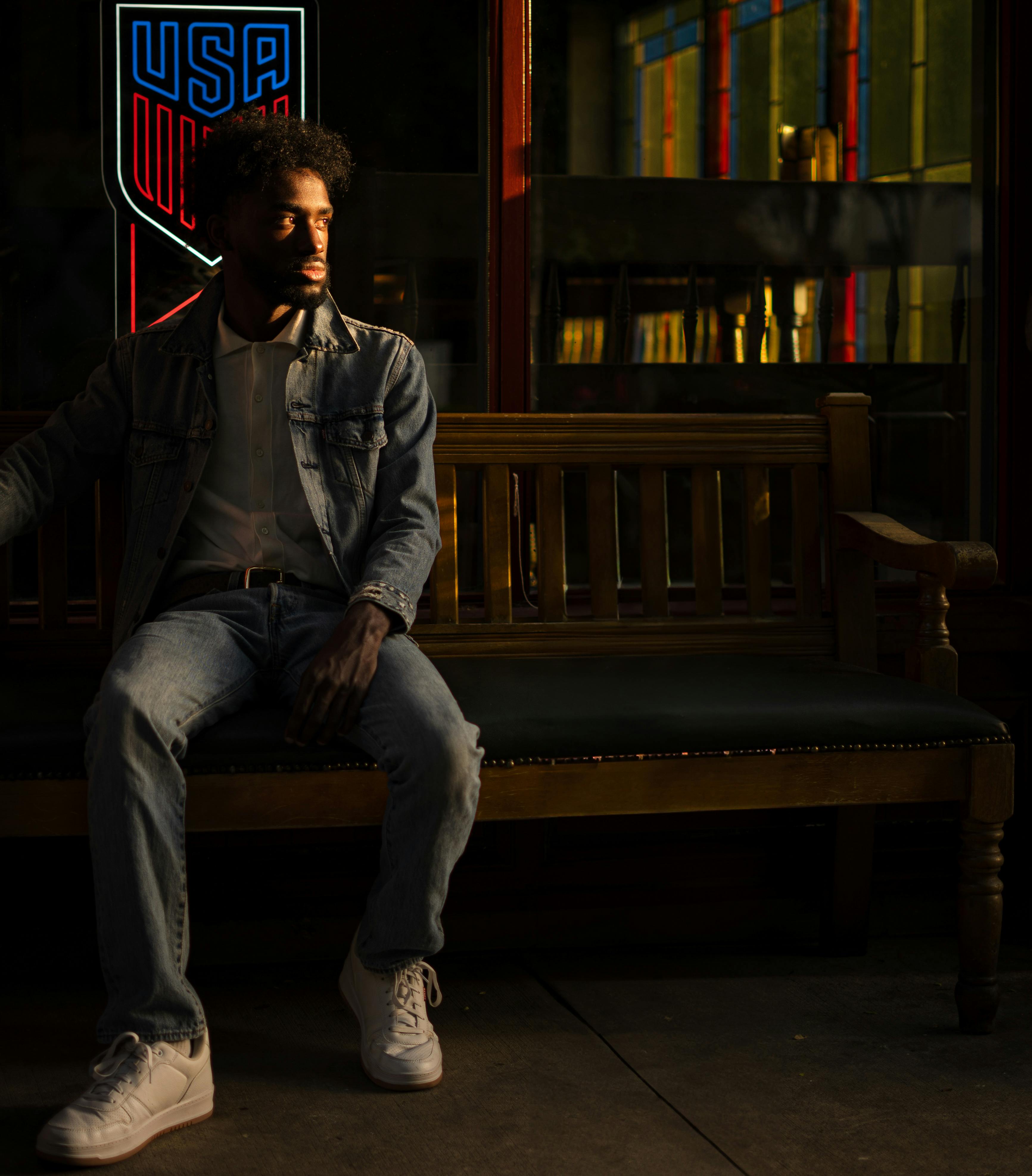 Young Man on Bench in Dimly Lit Room · Free Stock Photo