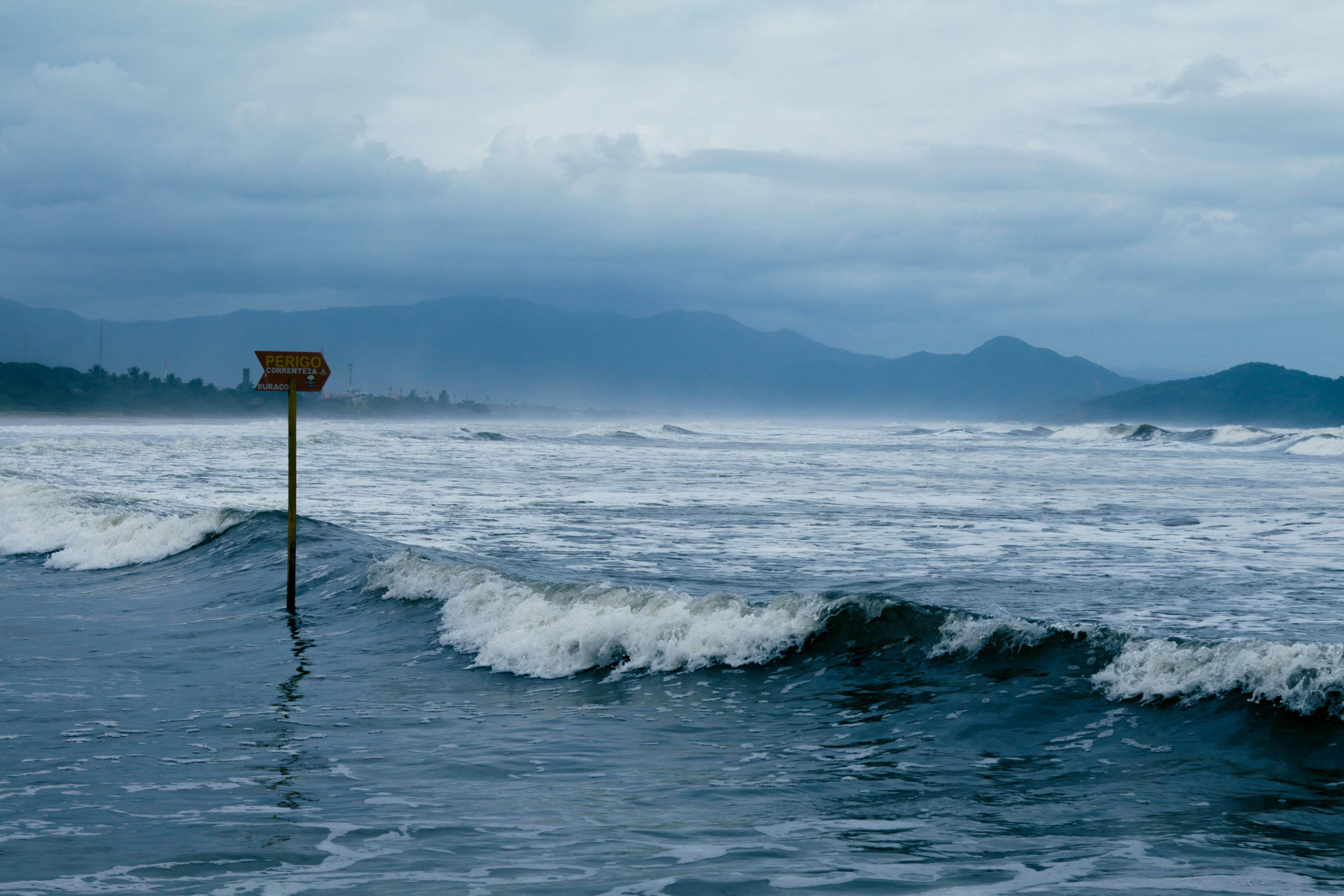 Ocean Warning Sign Amidst Cloudy Coastal Waves · Free Stock Photo