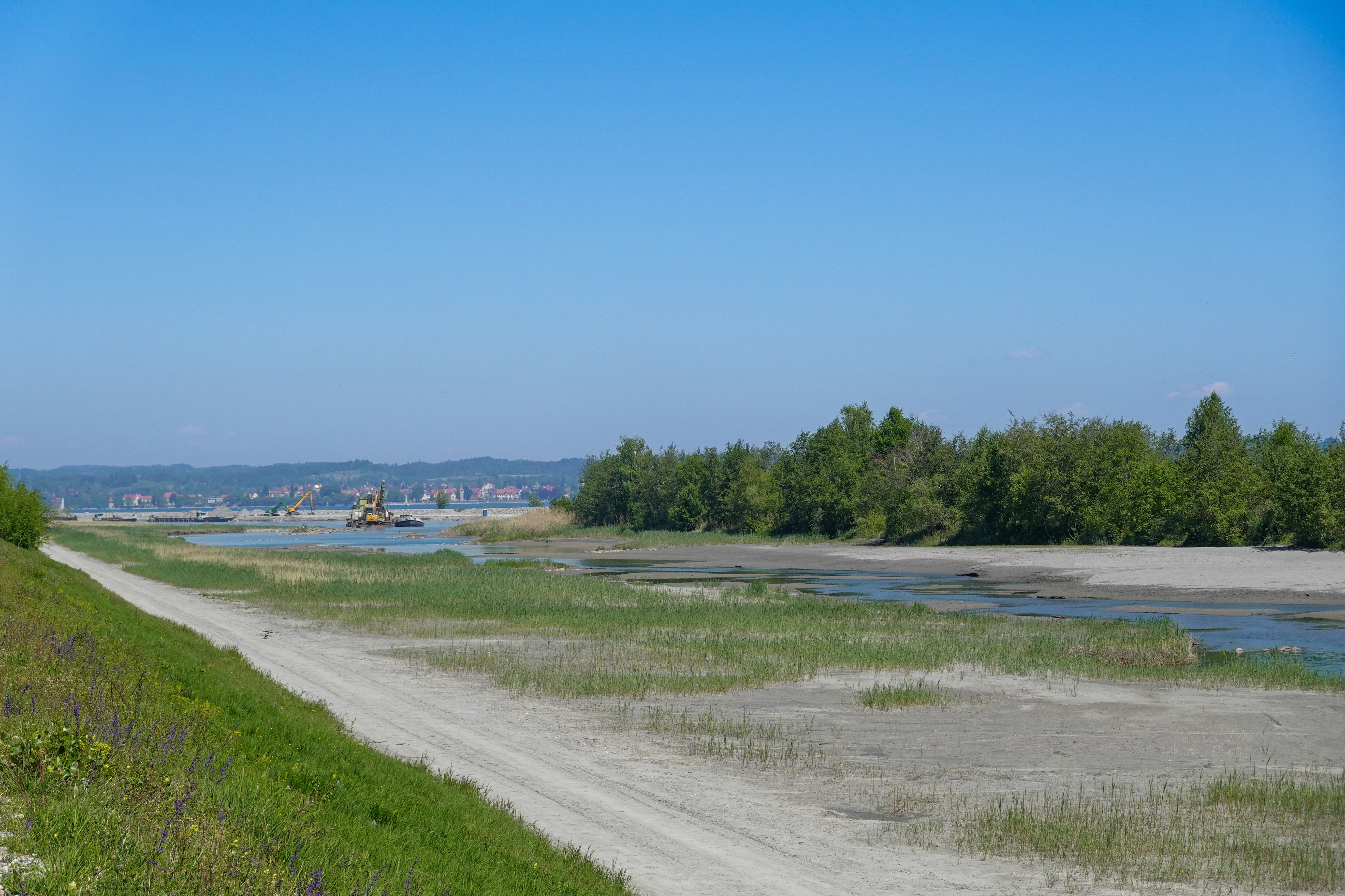 Scenic Riverbank View with Distant Construction Vehicles · Free Stock Photo