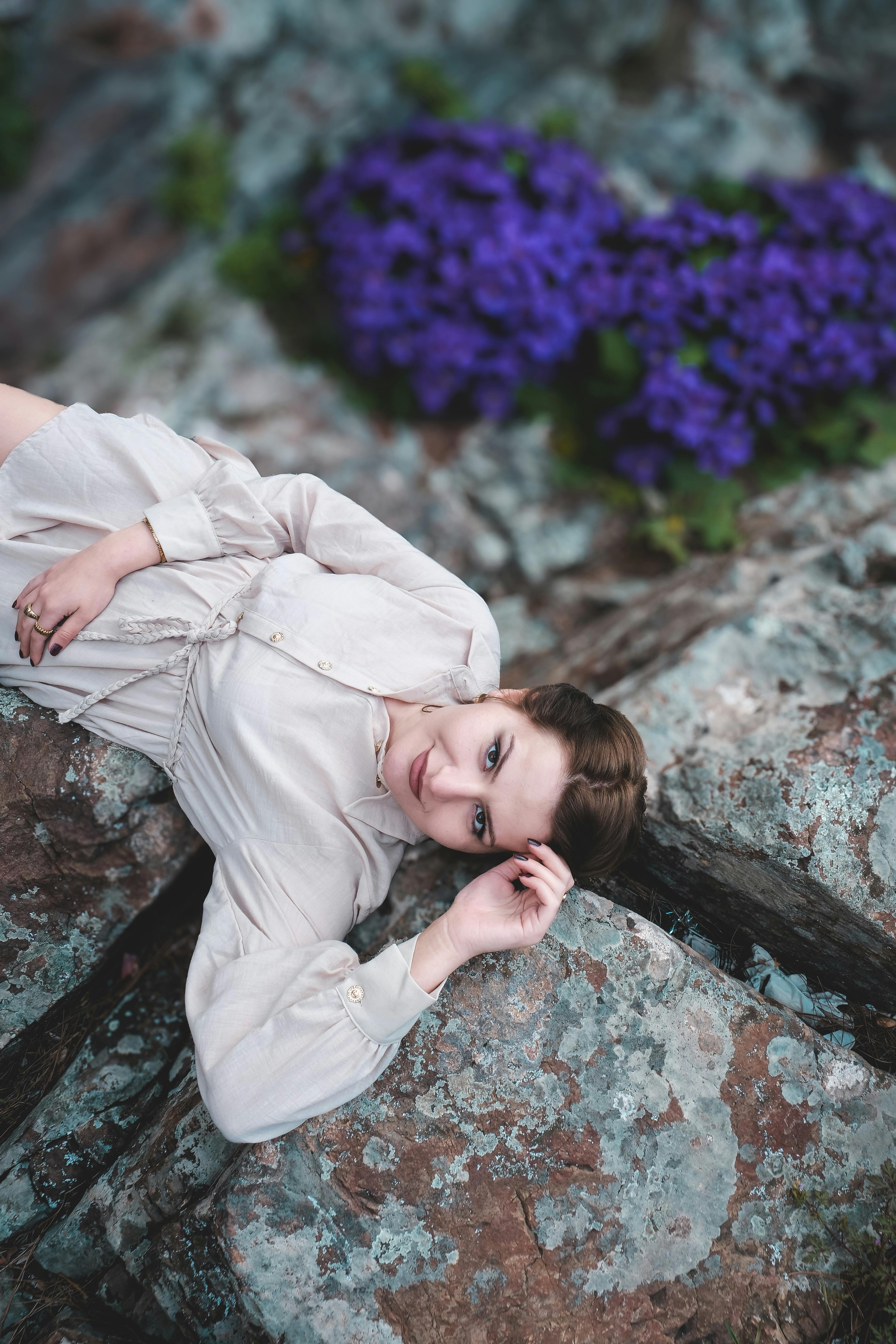 Elegant Woman Relaxing on Rocky Terrain with Flowers · Free Stock Photo