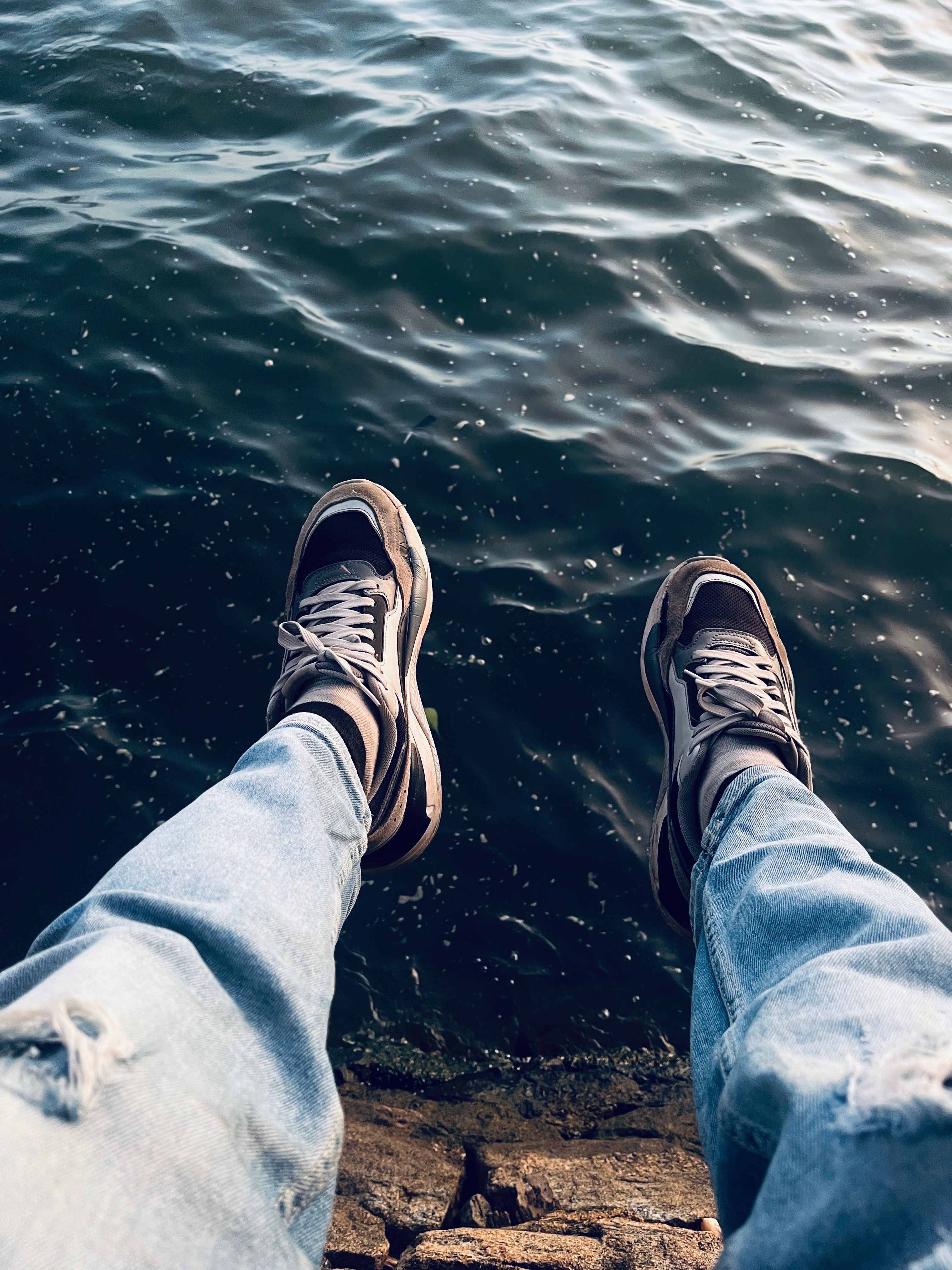 Casual Sneakers Dangling Over Water Edge · Free Stock Photo