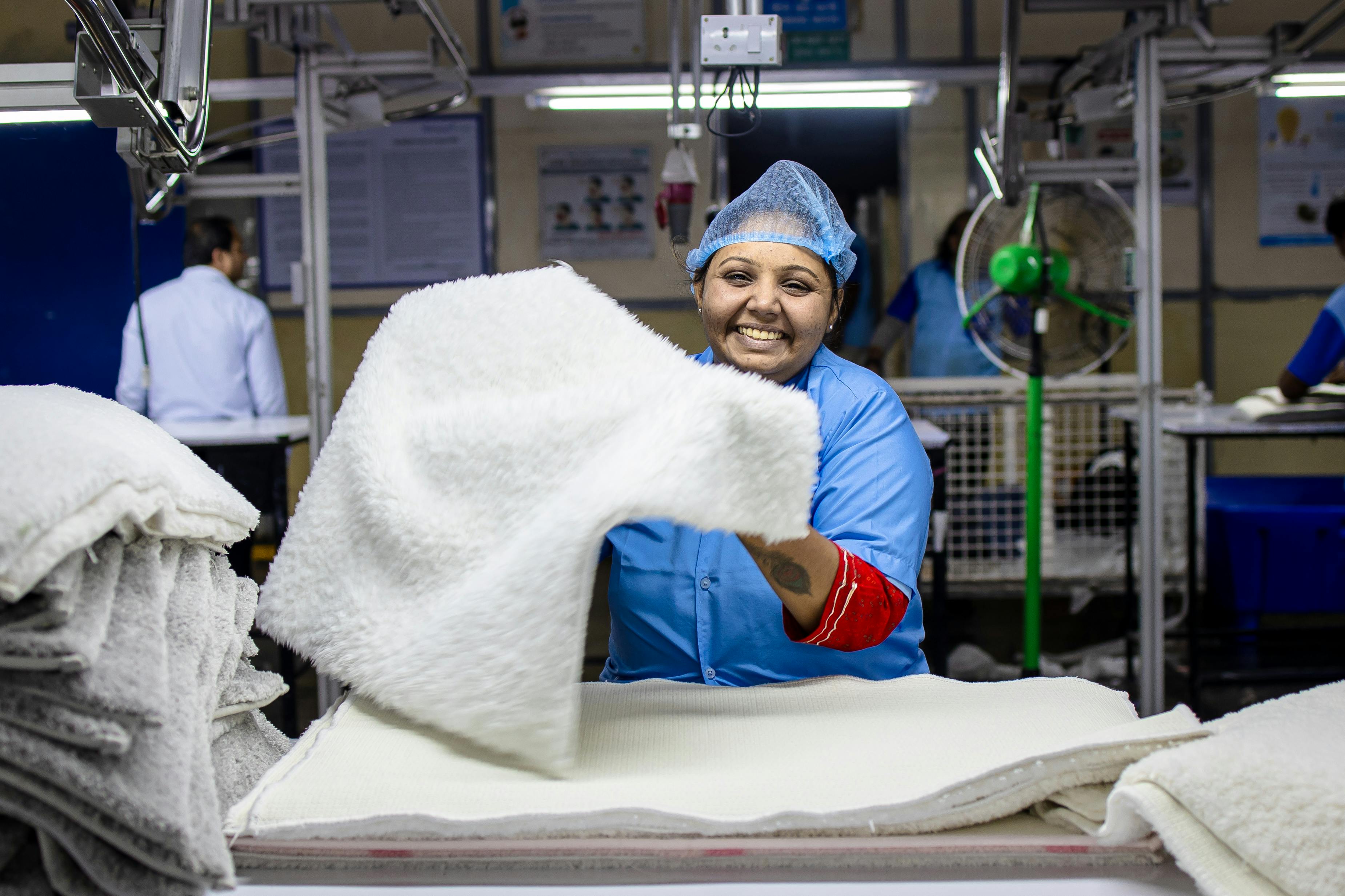 Smiling Factory Worker Handling Textiles Indoors · Free Stock Photo