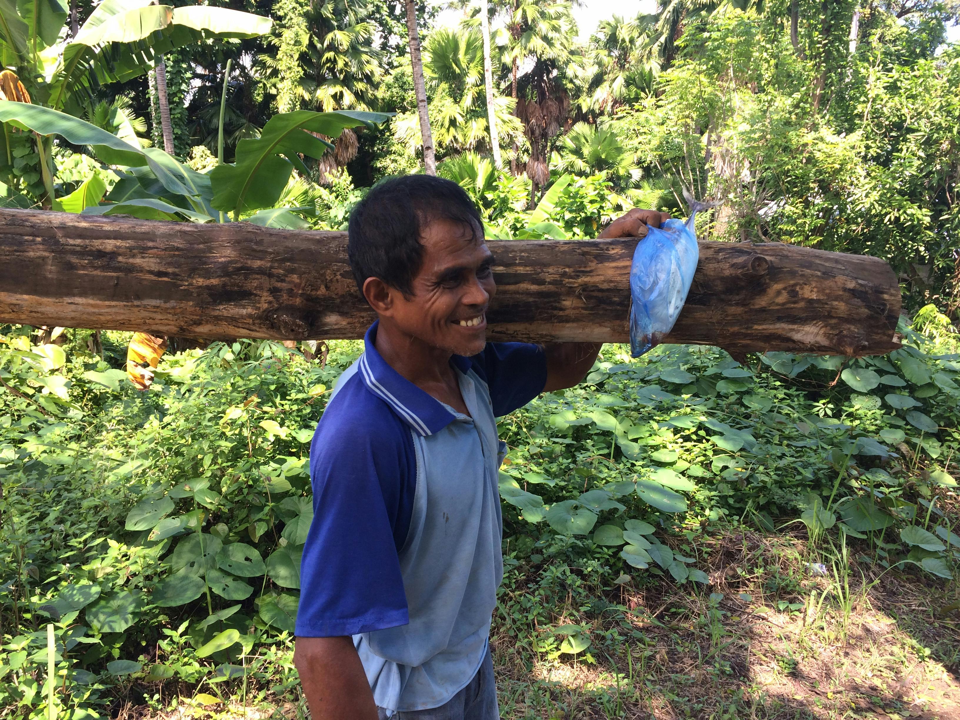 Smiling Man Carrying Log in Tropical Forest · Free Stock Photo