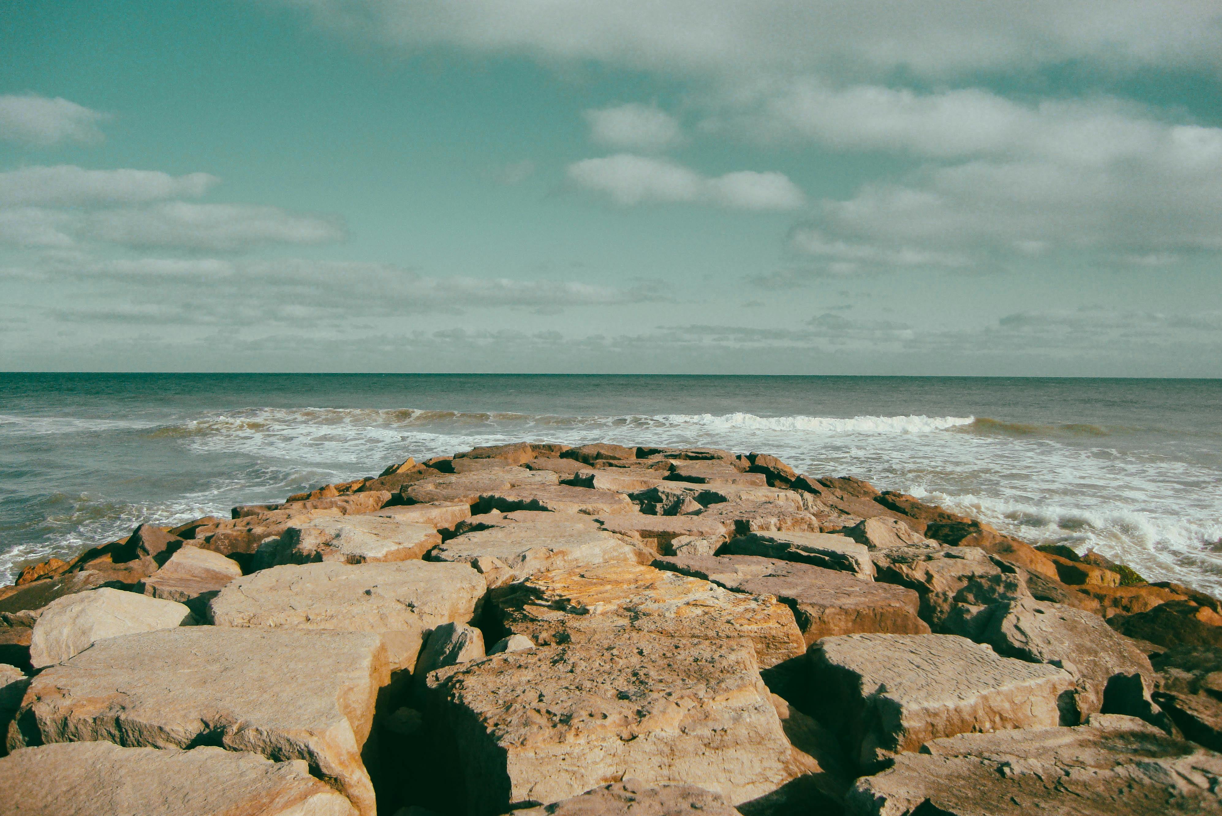 Rocky Jetty Leading to Ocean Under Clear Sky · Free Stock Photo