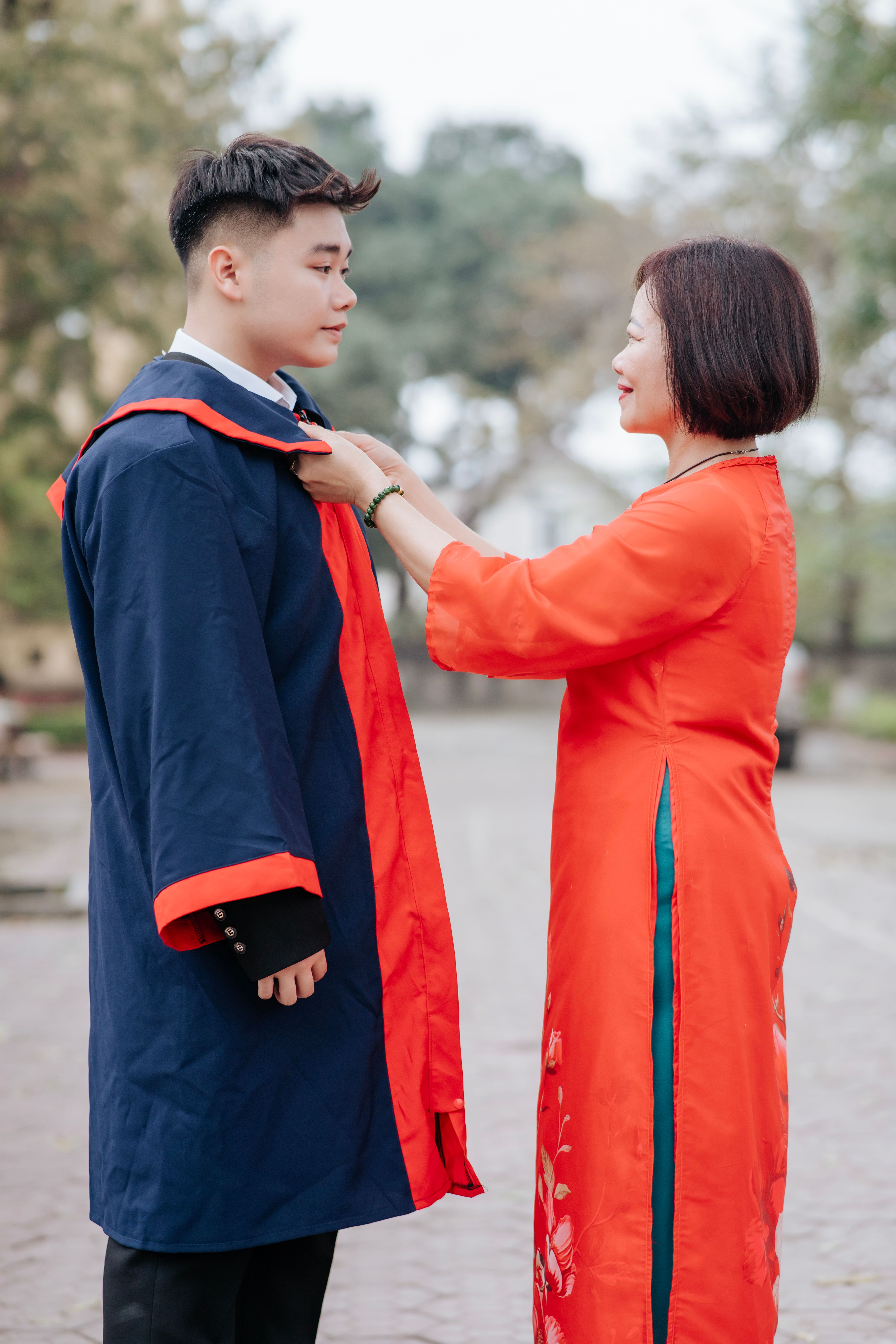 Mother Adjusting Son's Graduation Gown Outdoors · Free Stock Photo