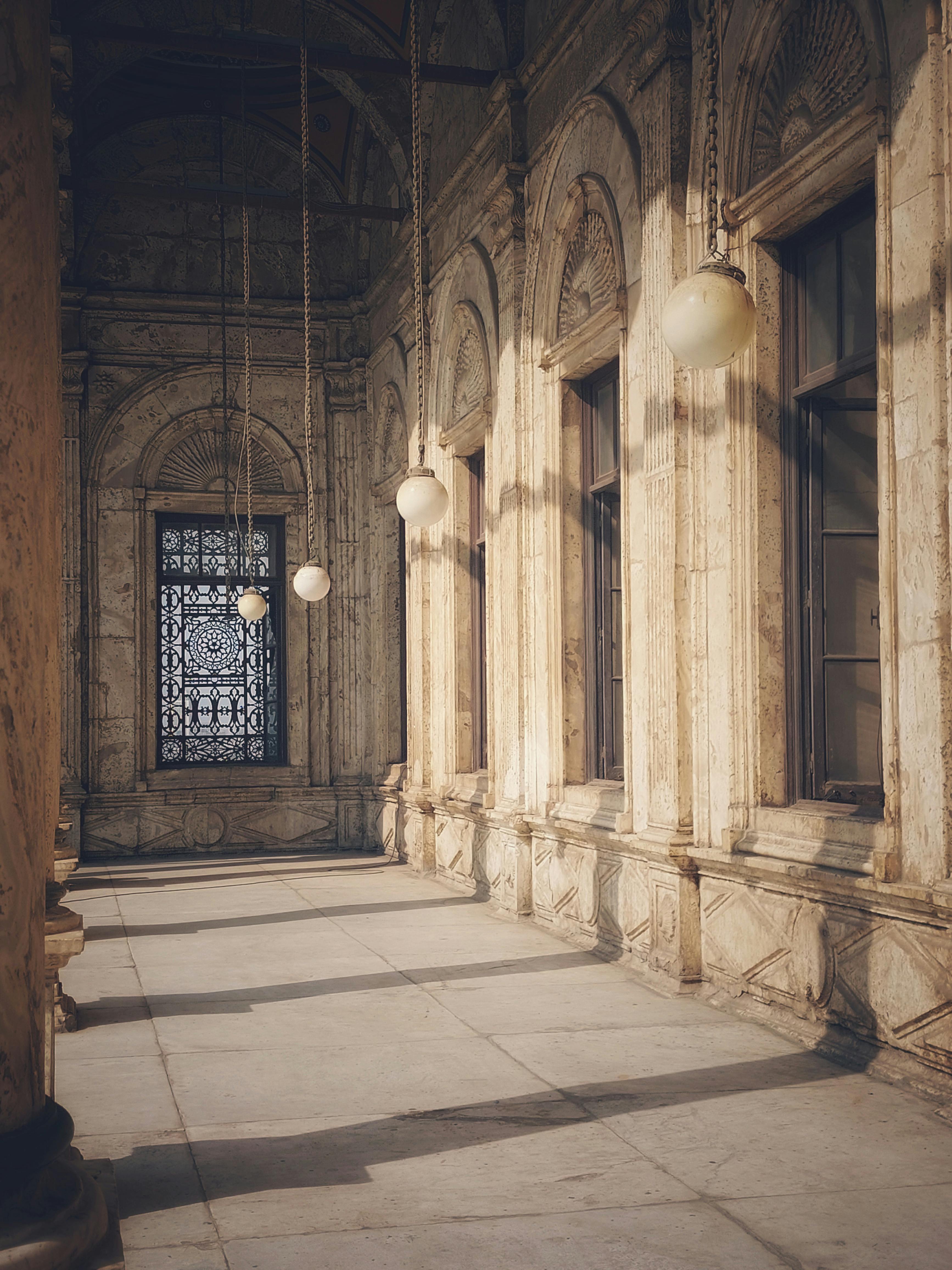 Sunlit Ancient Corridor with Arches and Lamps · Free Stock Photo