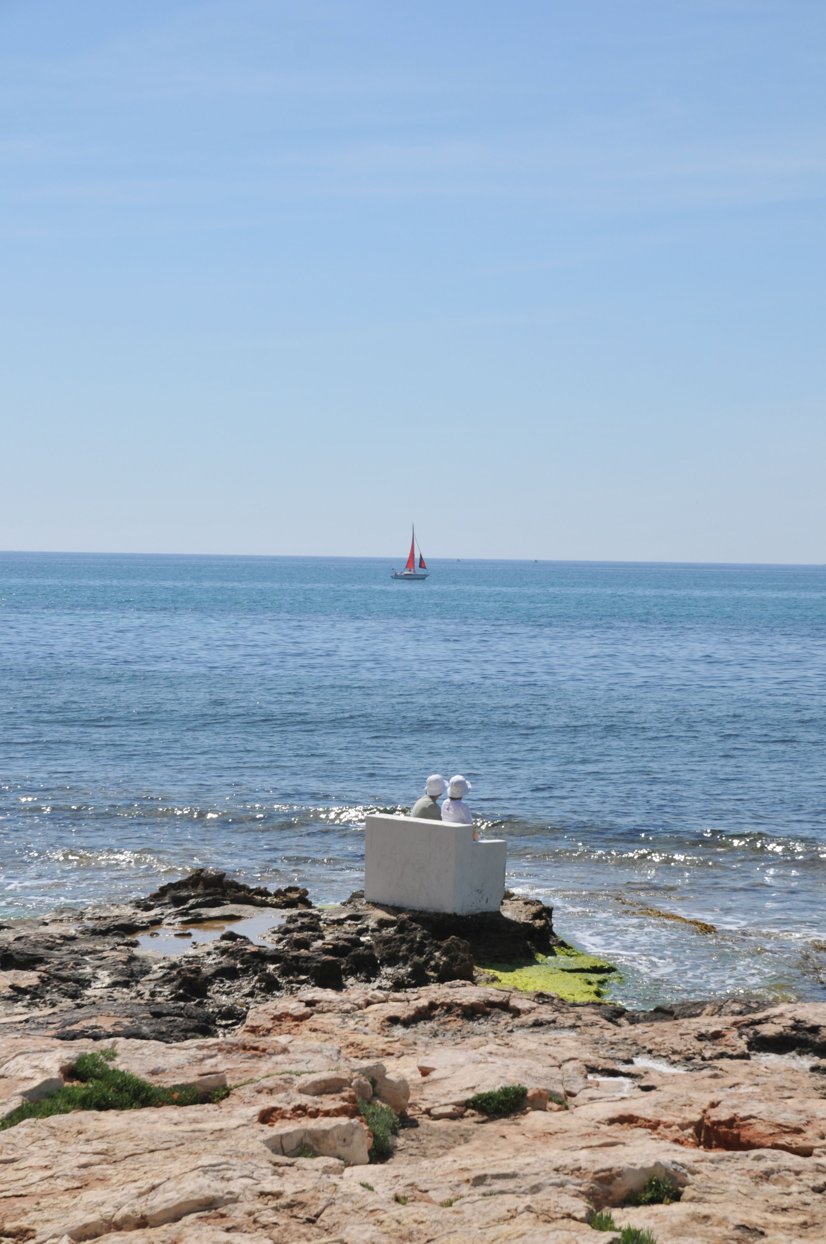 Peaceful Coastal View with Distant Red Sailboat · Free Stock Photo