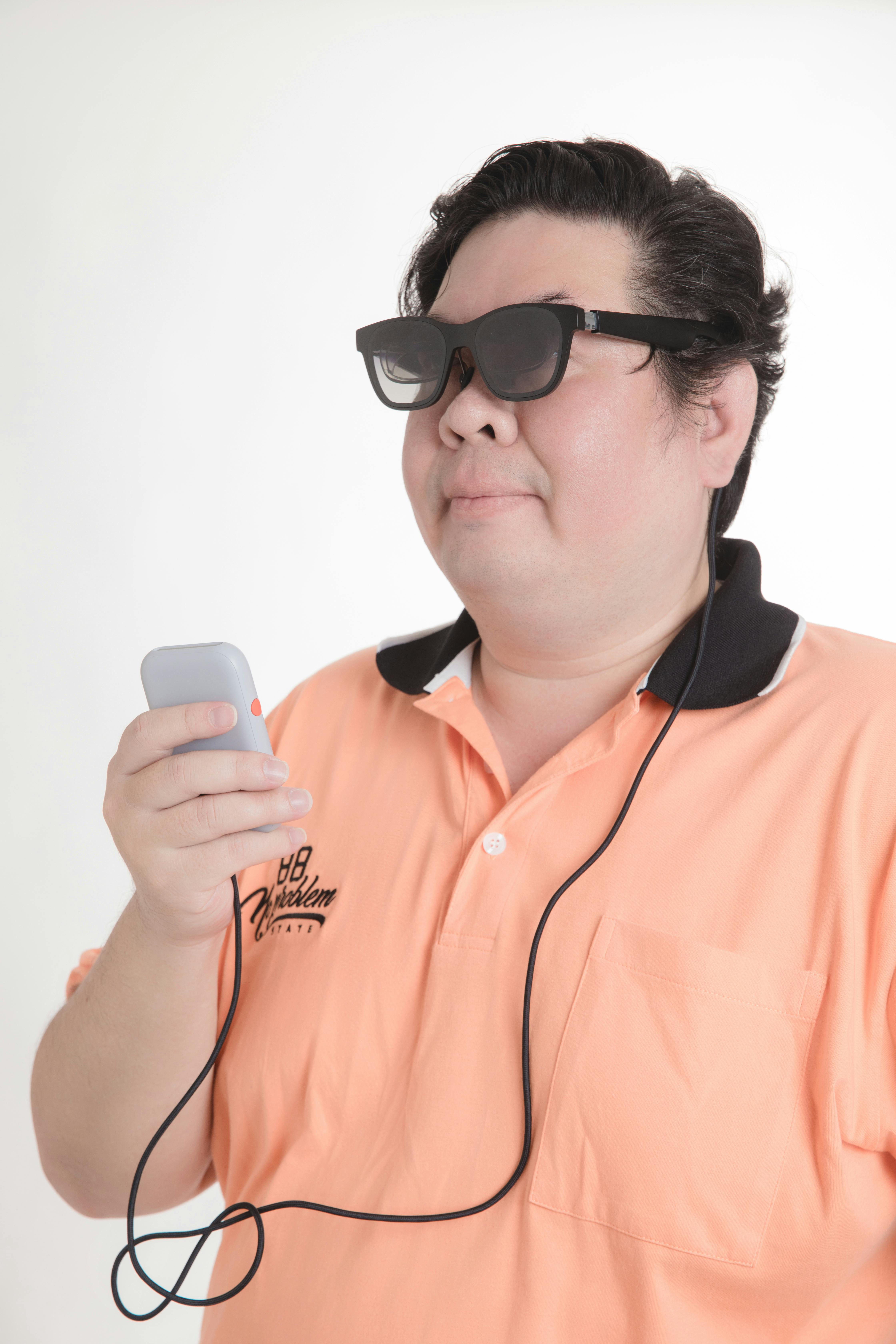 Man in Orange Polo with Sunglasses and Device · Free Stock Photo