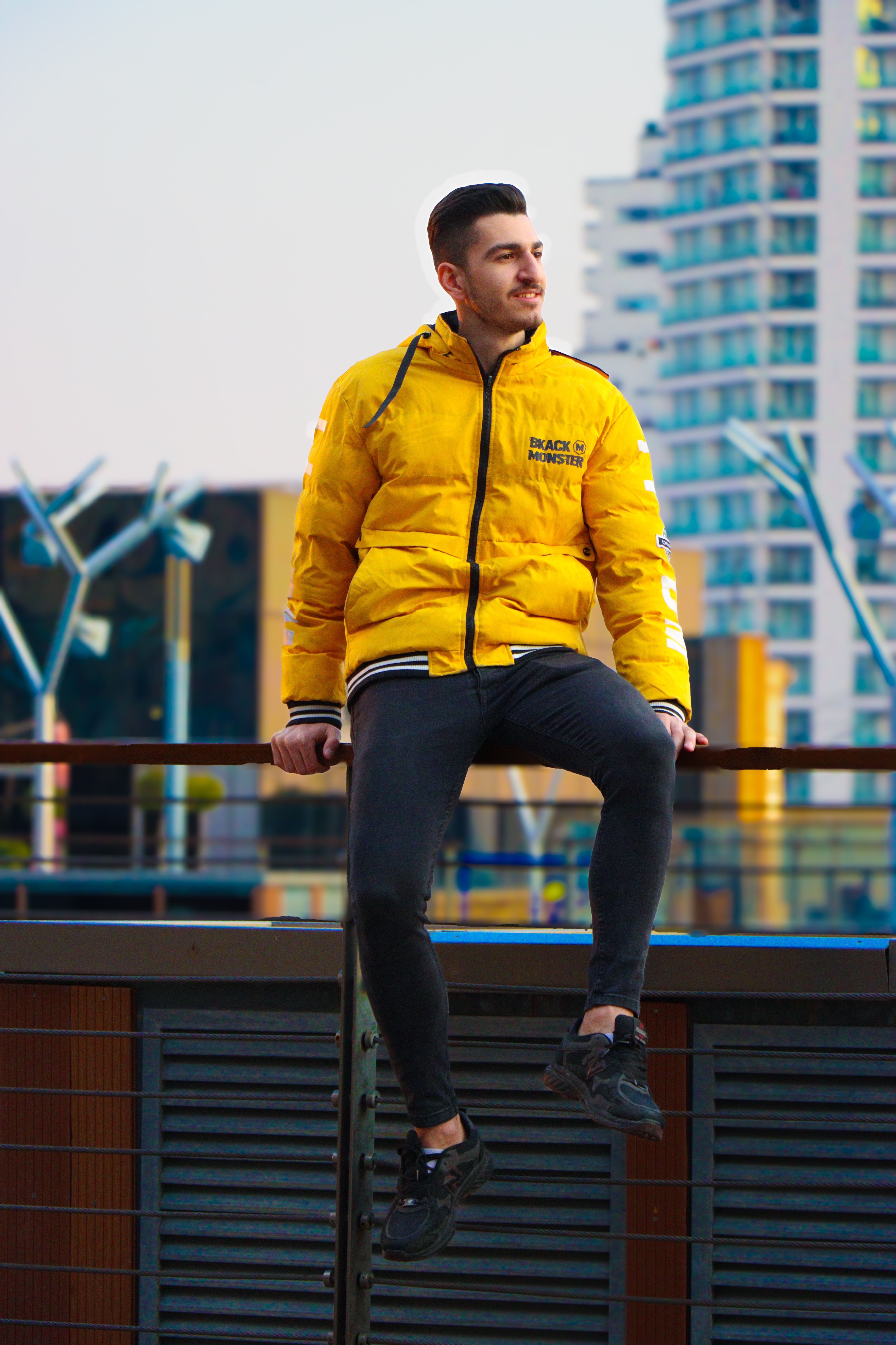 Man in Yellow Jacket Sitting on Rail Outdoors · Free Stock Photo