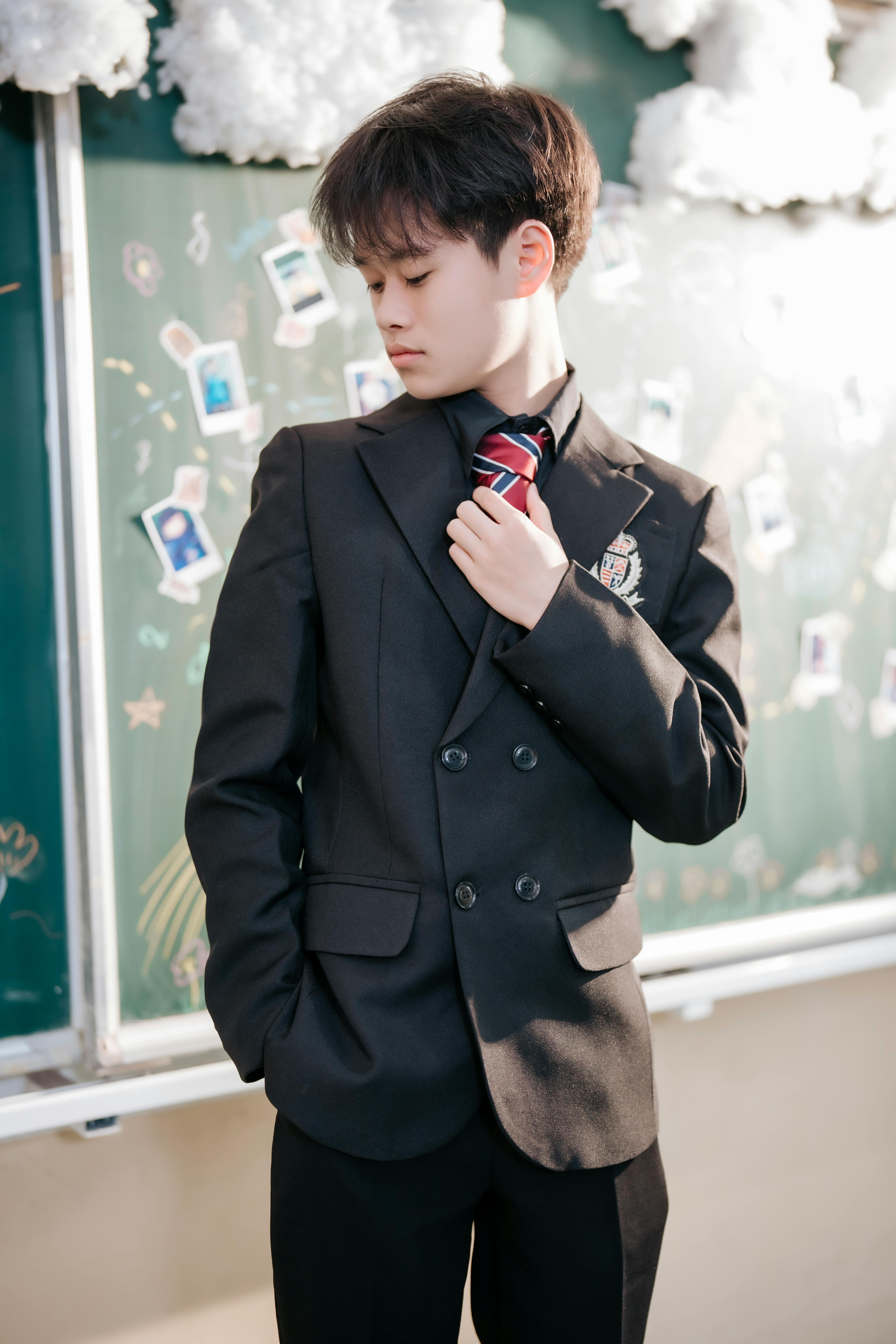 Young Student in Uniform Adjusting Tie in Classroom · Free Stock Photo