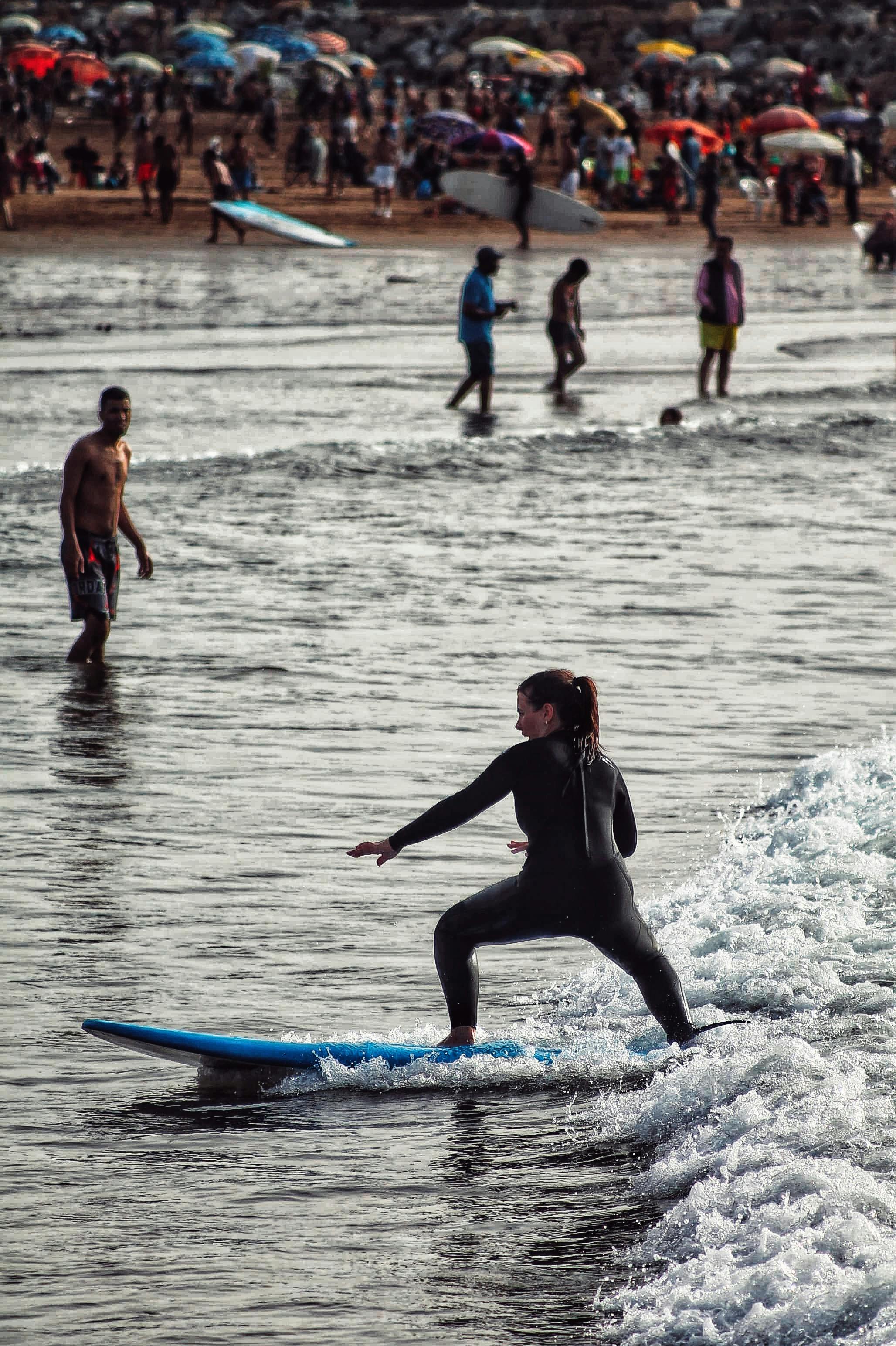 Surfer Riding Waves at a Busy Beach · Free Stock Photo