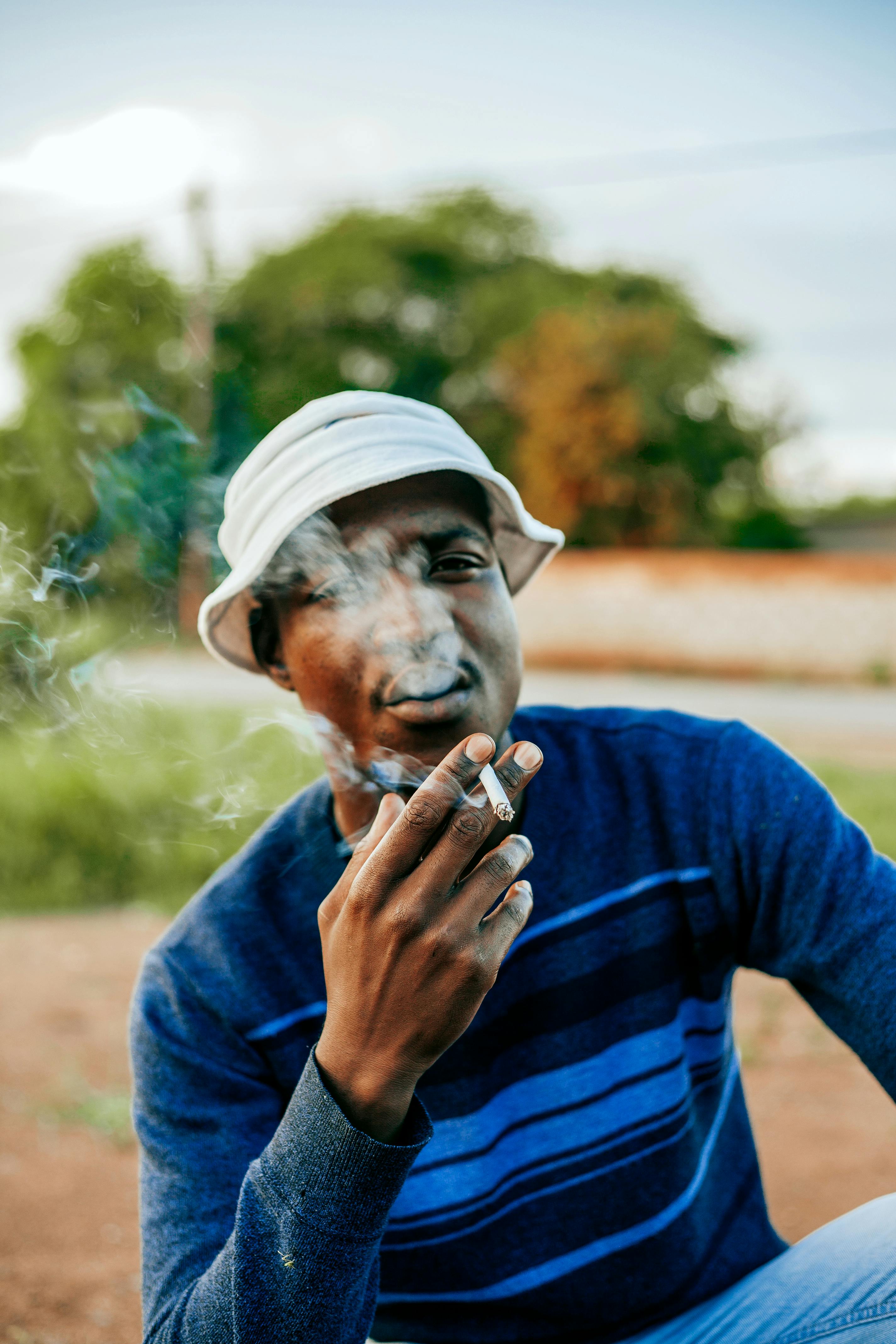 Man in Bucket Hat Smoking Outdoors in Gaborone · Free Stock Photo