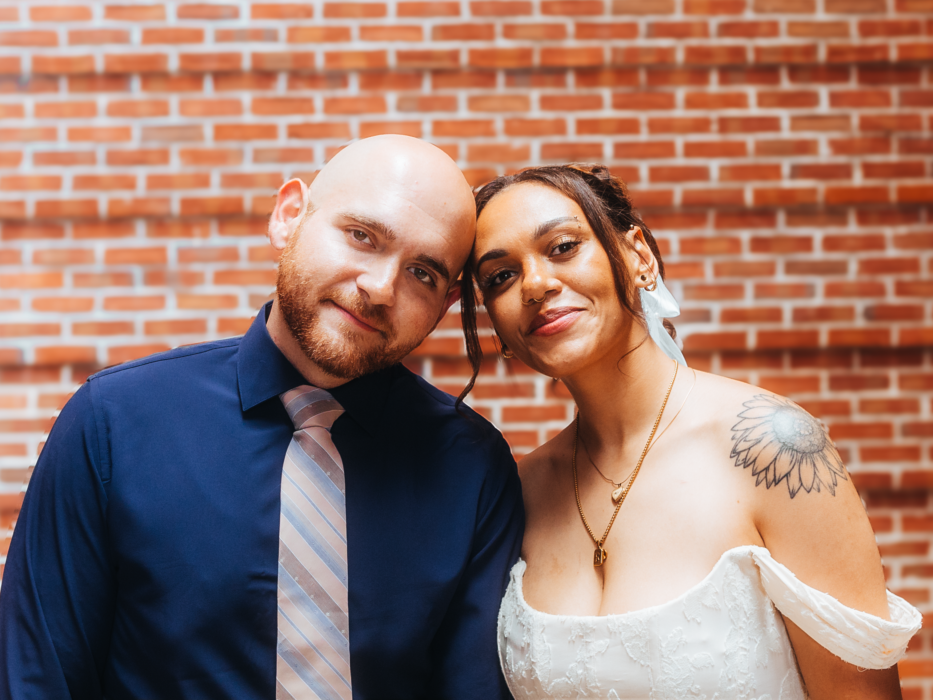 Smiling couple standing together against brick wall · Free Stock Photo
