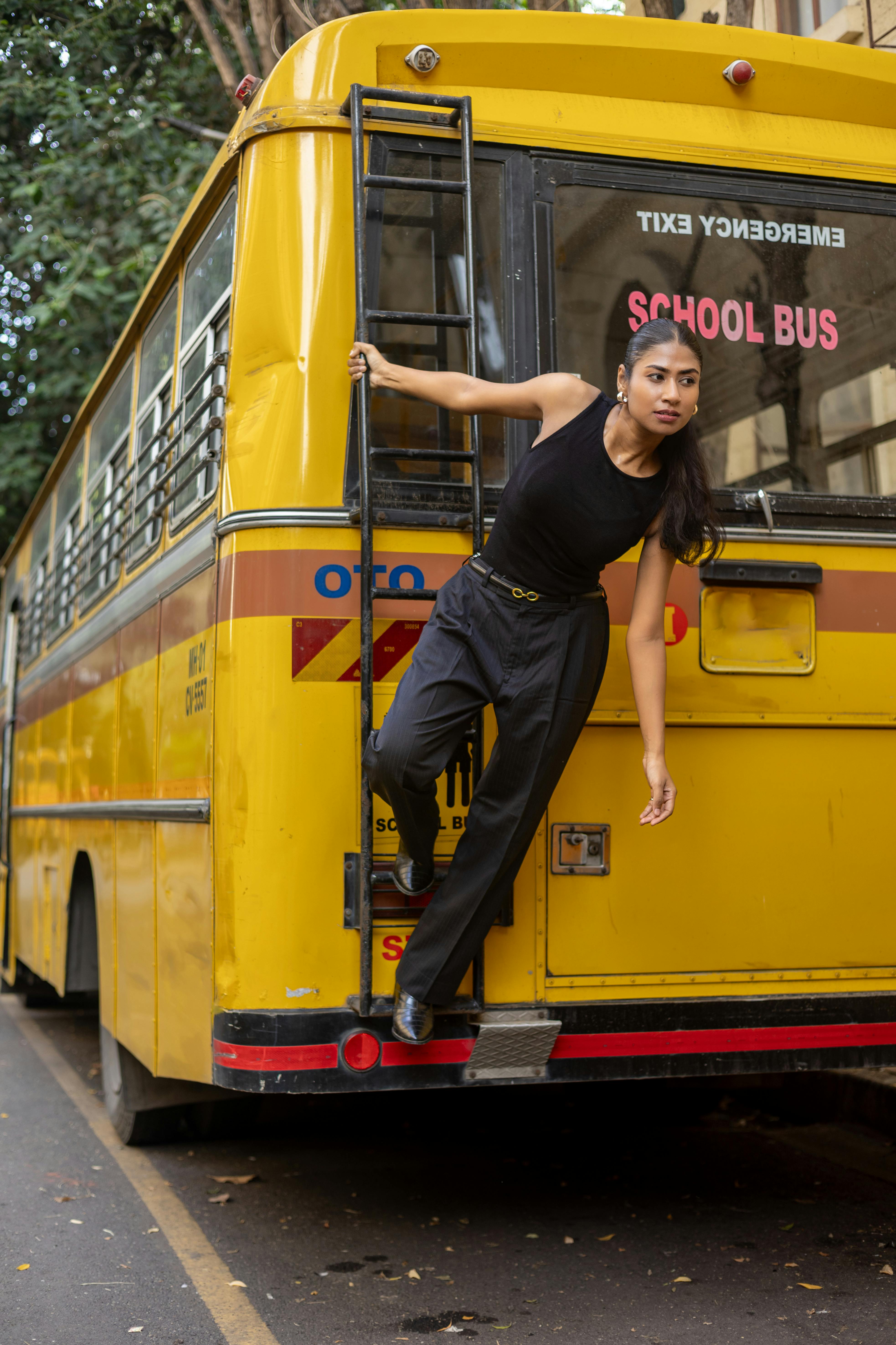 Young Woman Posing on School Bus Ladder Outdoors · Free Stock Photo