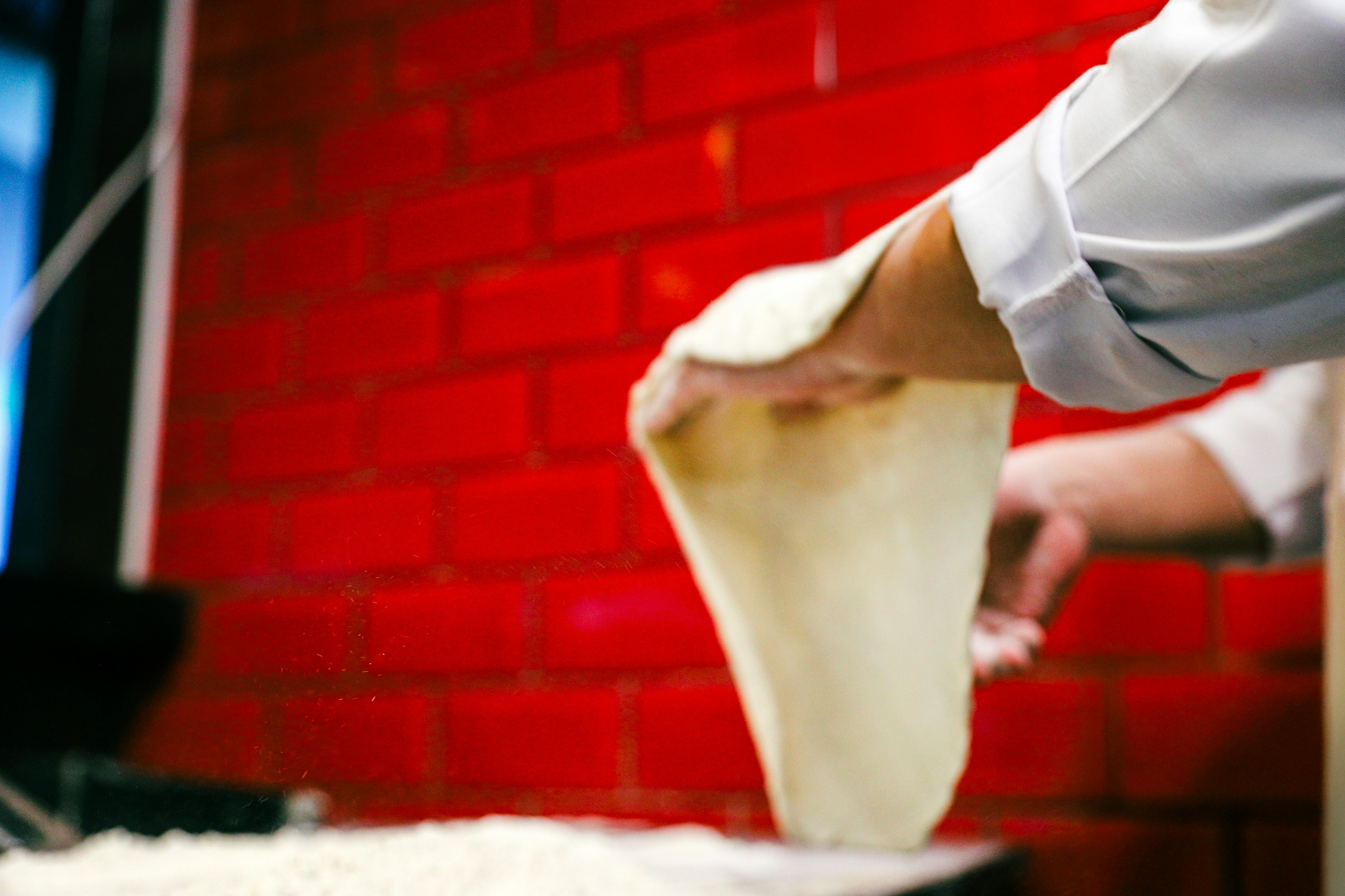 Chef Stretching Pizza Dough in Rustic Kitchen · Free Stock Photo