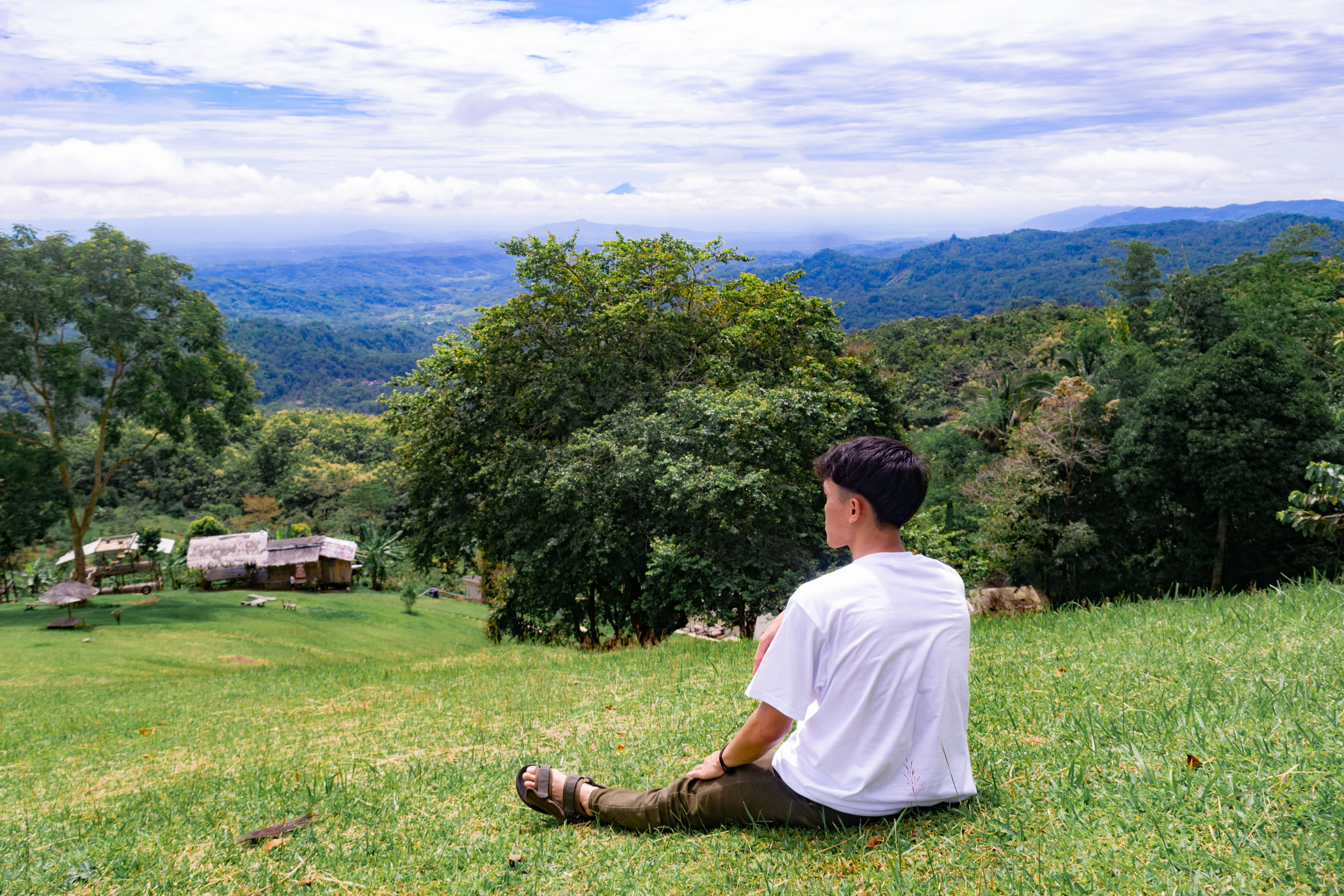 Man Sitting on Hill Overlooking Scenic Landscape · Free Stock Photo