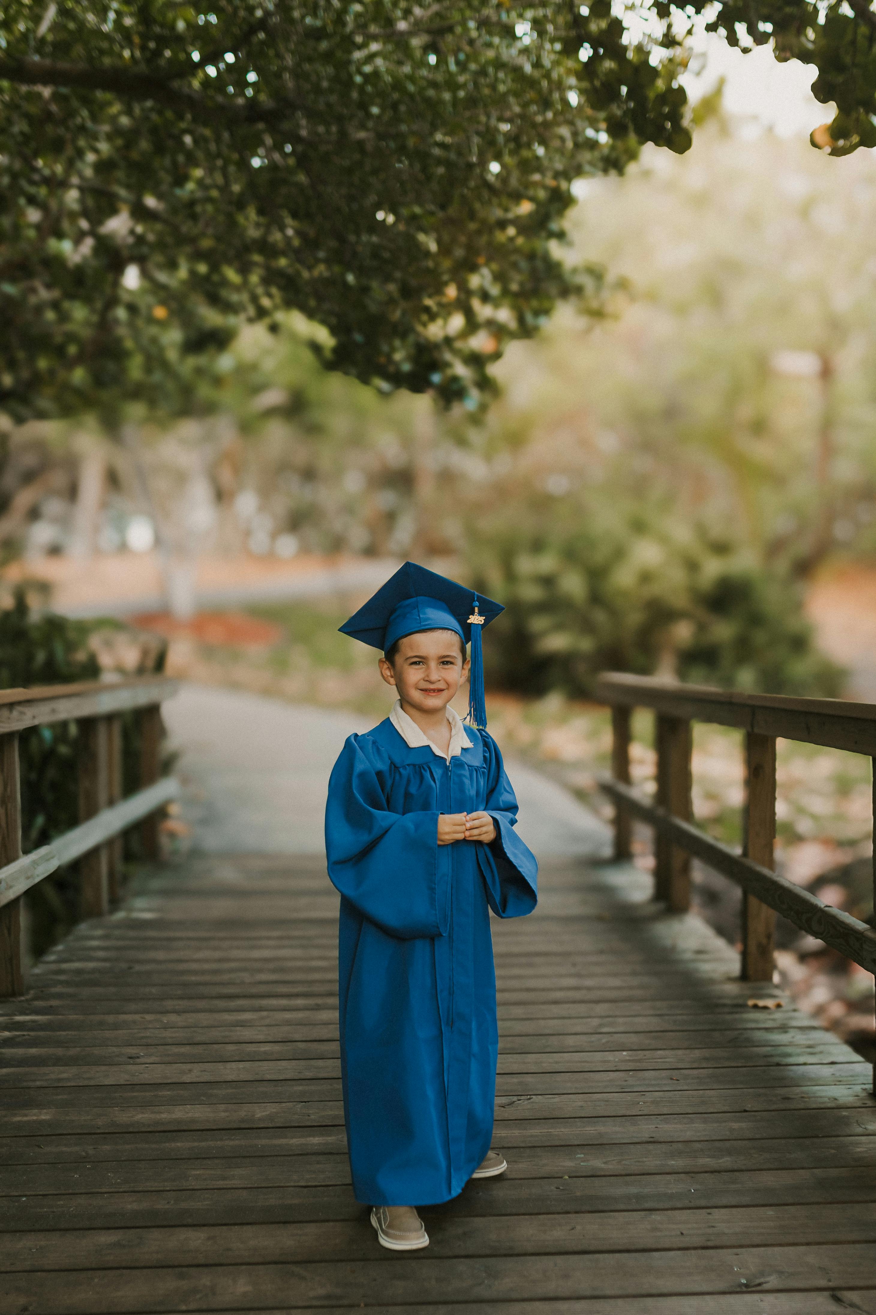 Child Graduate in Blue Gown on Wooden Bridge · Free Stock Photo