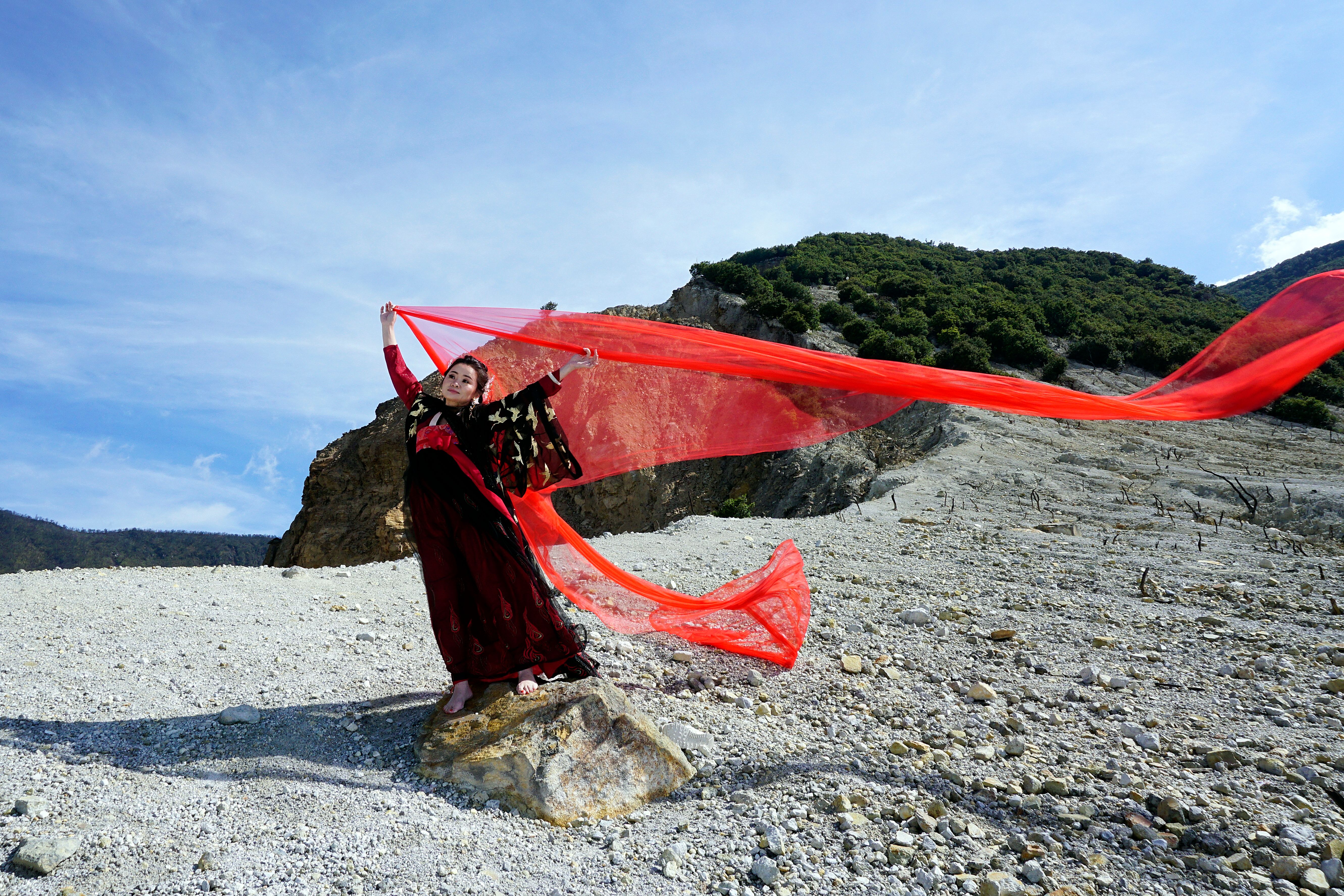 Woman in Flowing Red Scarf on Rocky Terrain · Free Stock Photo