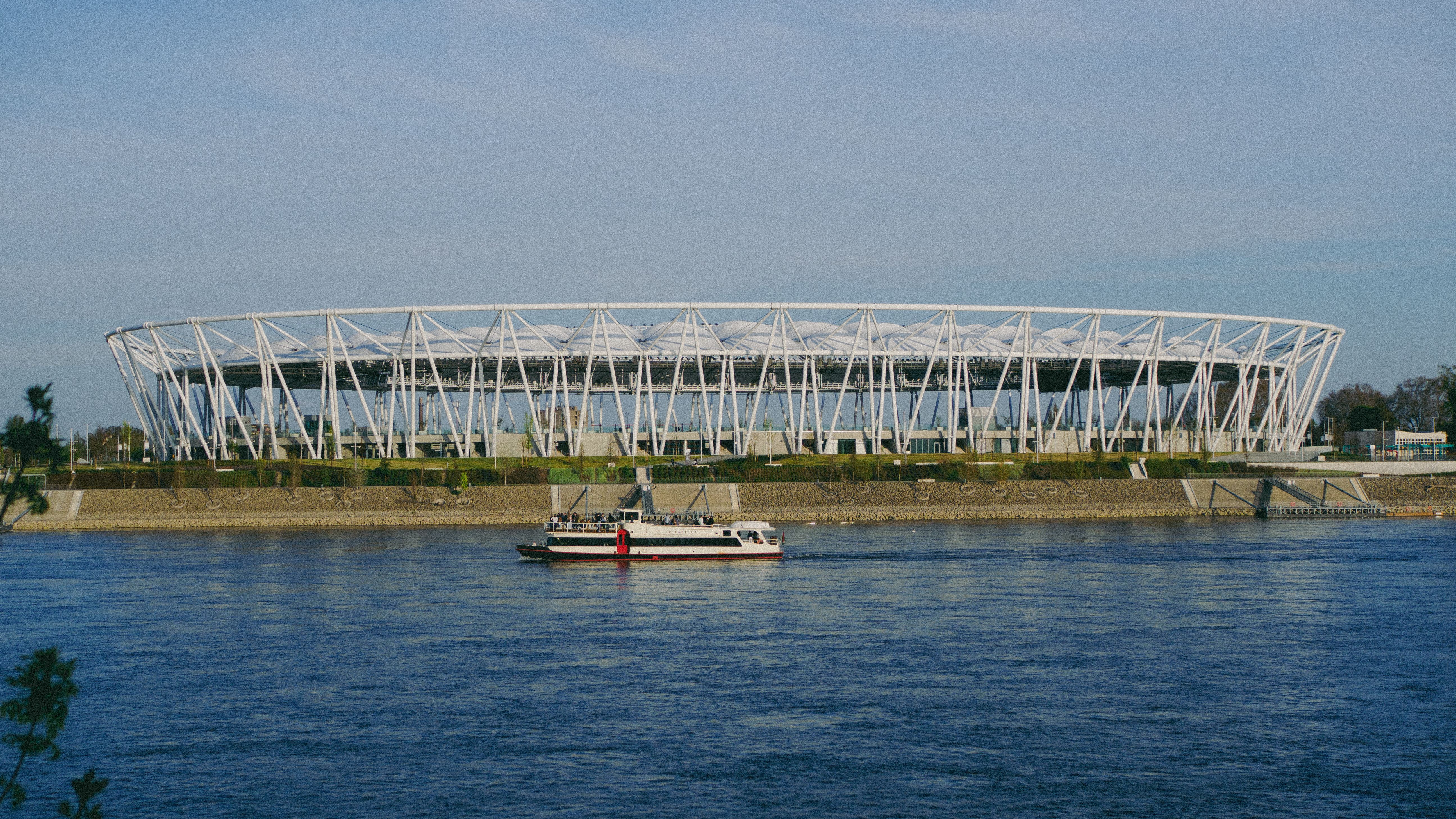 Modern Stadium by River with Passing Ferry · Free Stock Photo