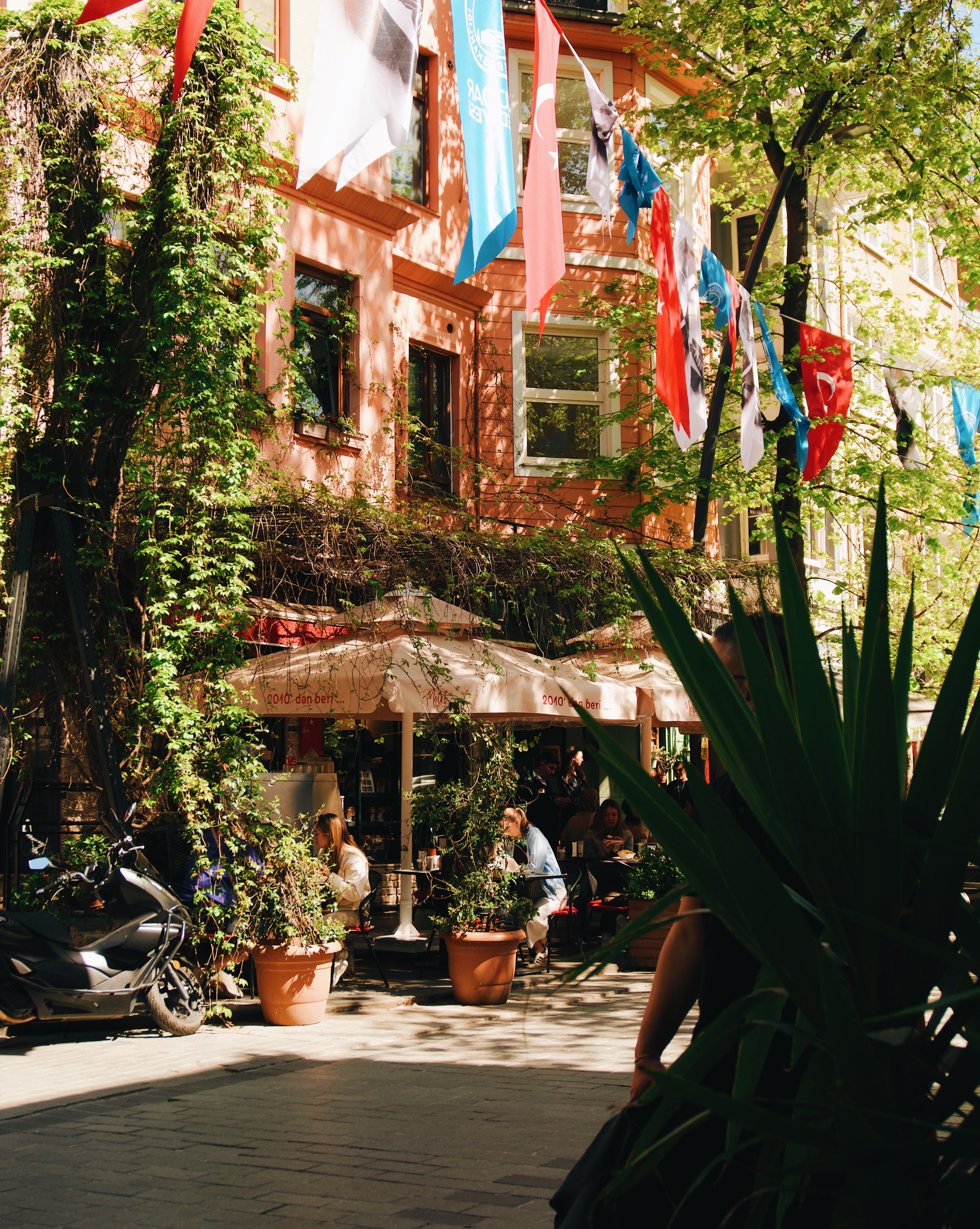 Charming Outdoor Cafe with Colorful Flags in Sunlight · Free Stock Photo