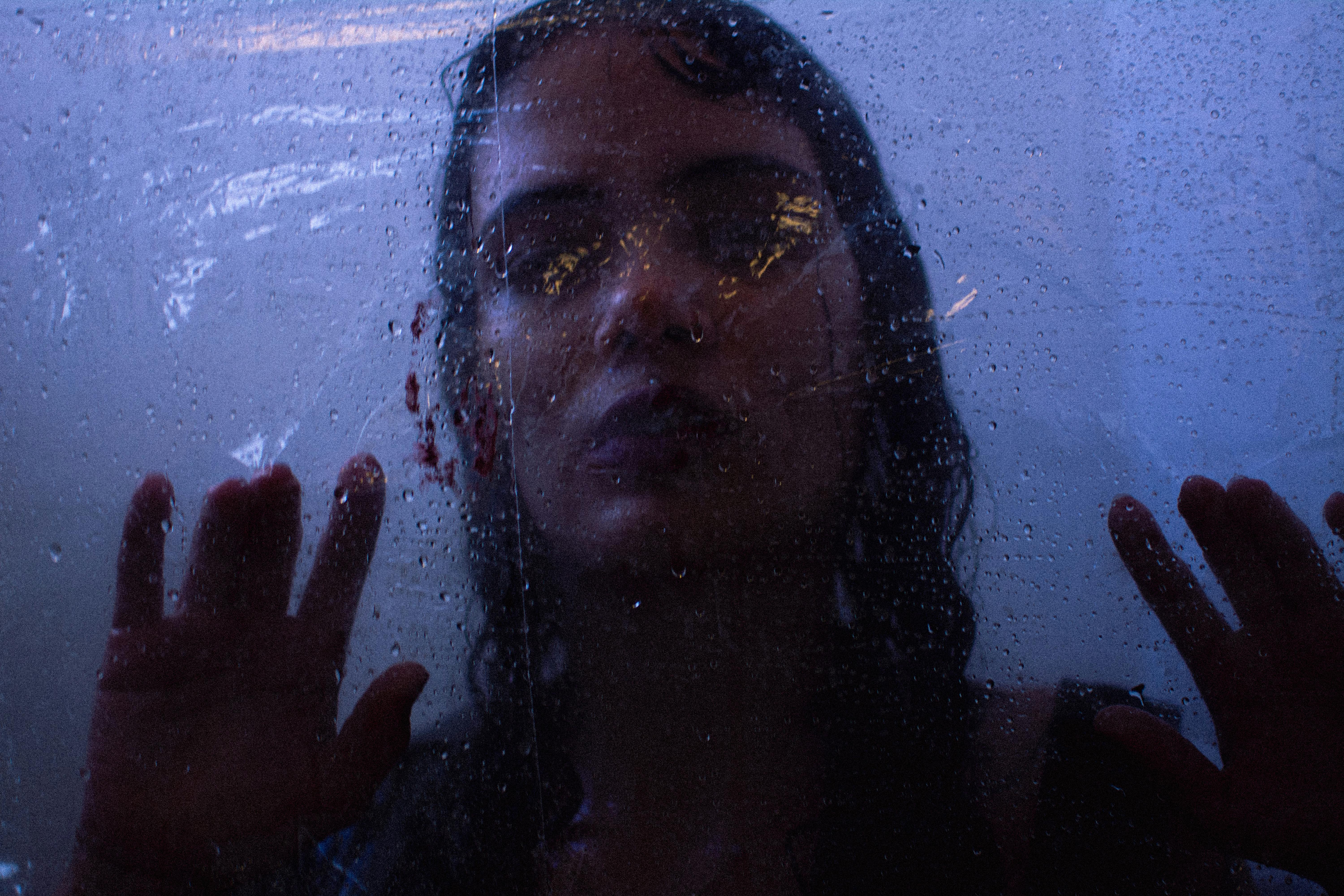 Moody Portrait Behind a Rain-Splashed Window · Free Stock Photo