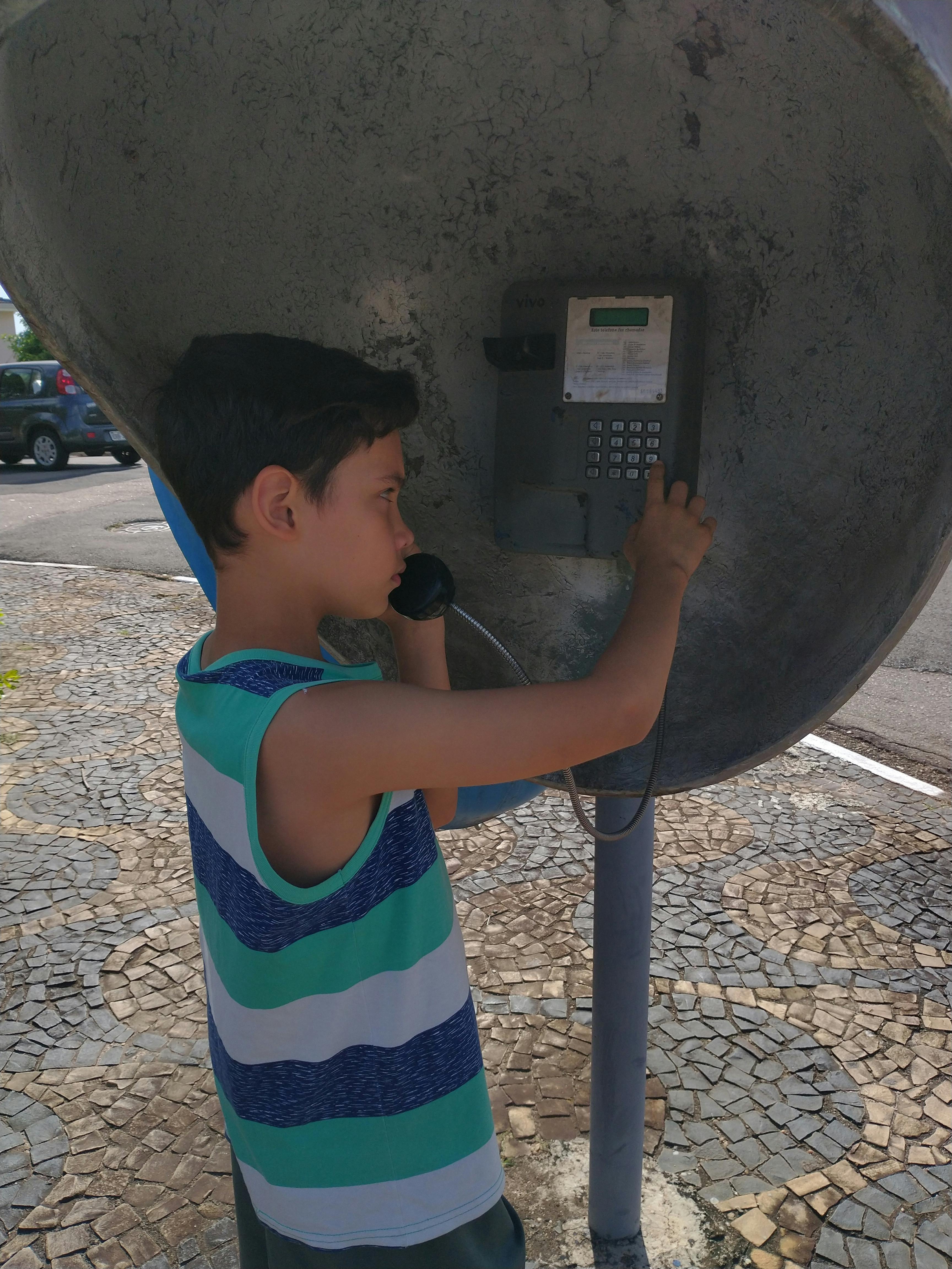 Young Boy Using Vintage Public Telephone Outdoors · Free Stock Photo