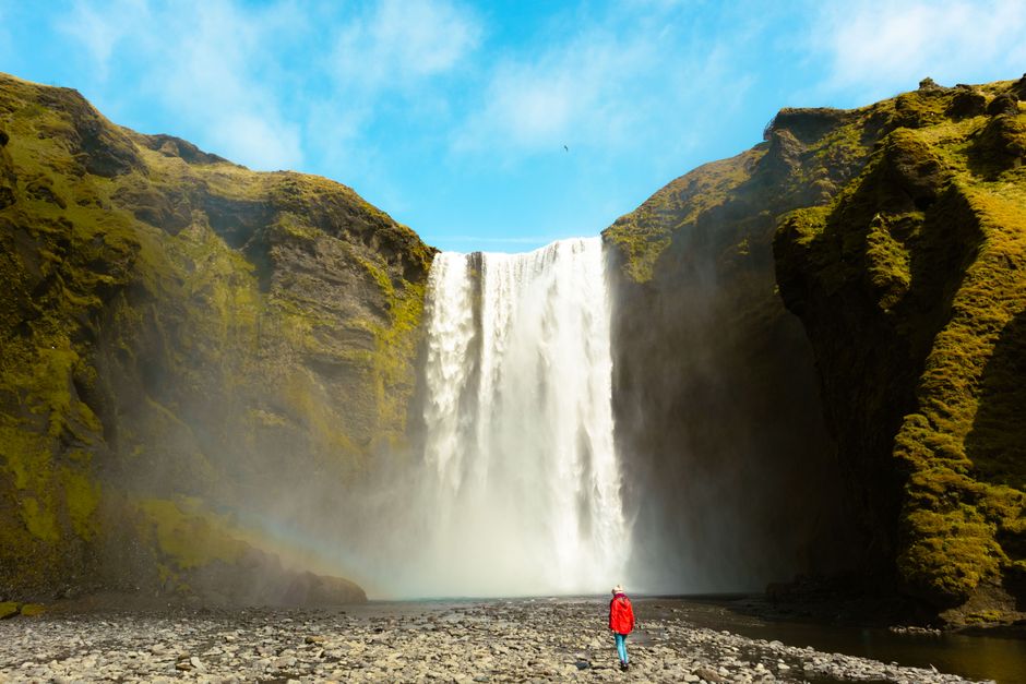 Dramatic view of Skogafoss waterfall with person in red coat in Iceland.