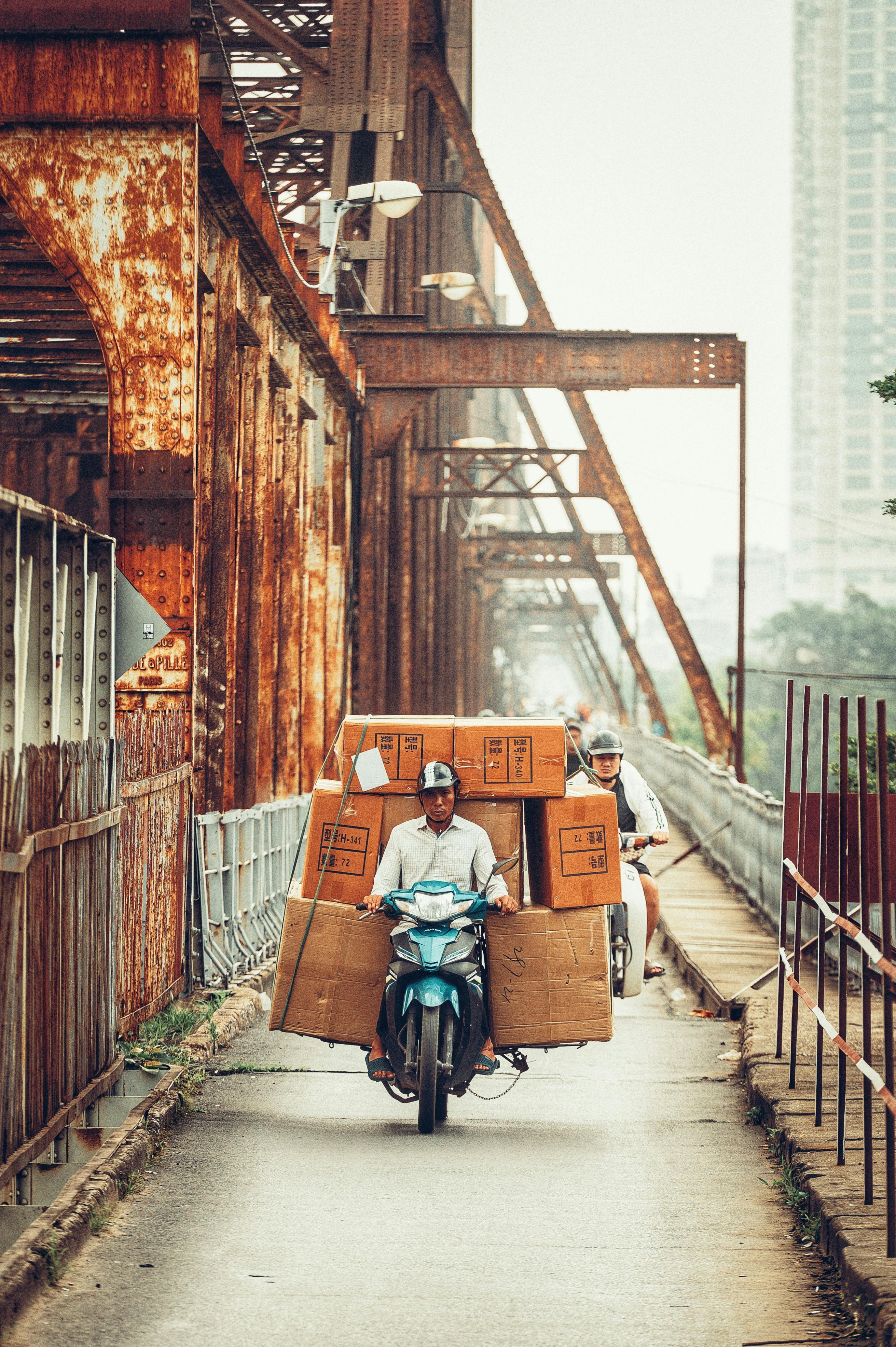 Motorcyclist Delivering Boxes on Rusty Bridge · Free Stock Photo