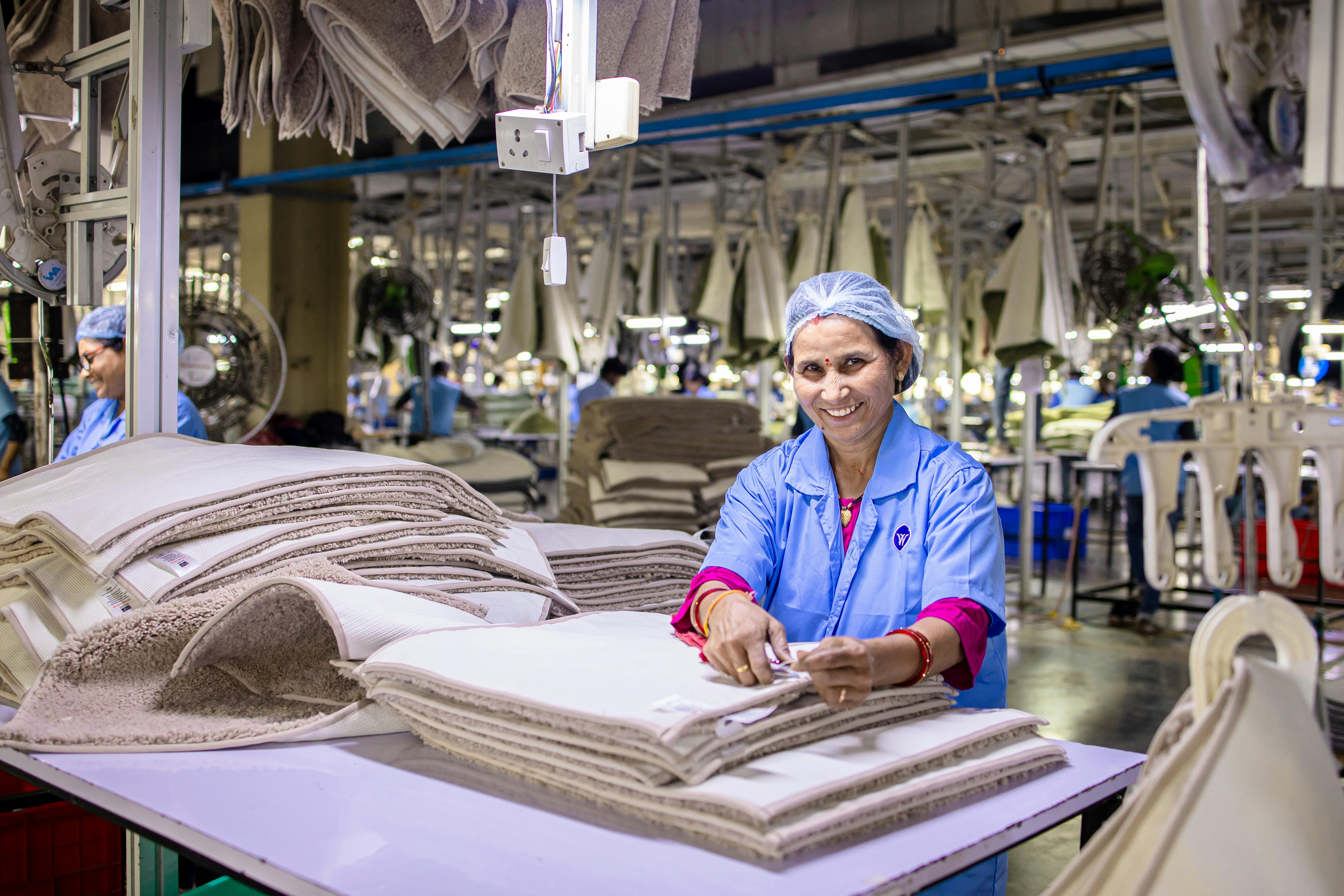Smiling Factory Worker Folding Textiles · Free Stock Photo