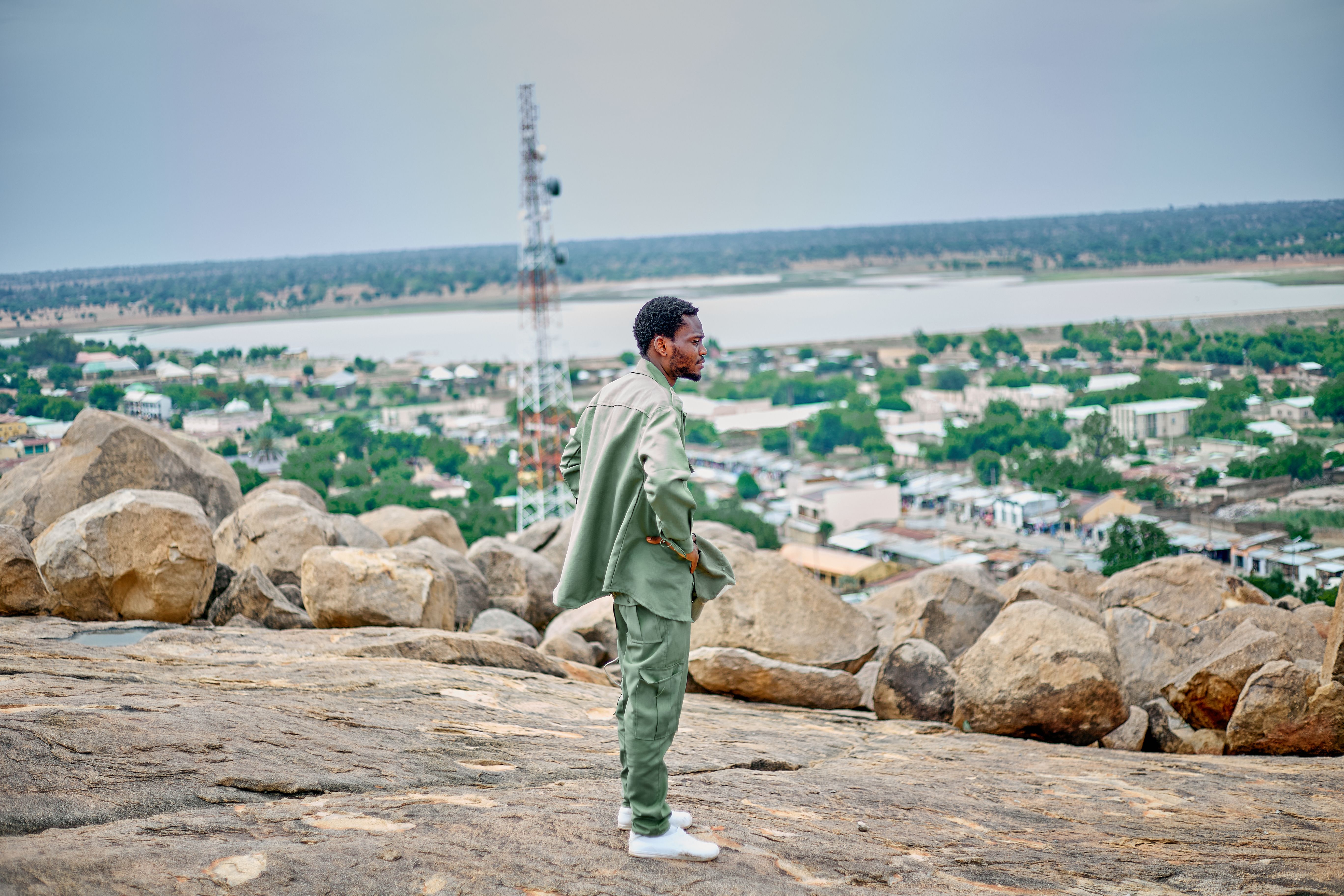 Man Standing on Rocky Hill Overlooking Village Landscape · Free Stock Photo