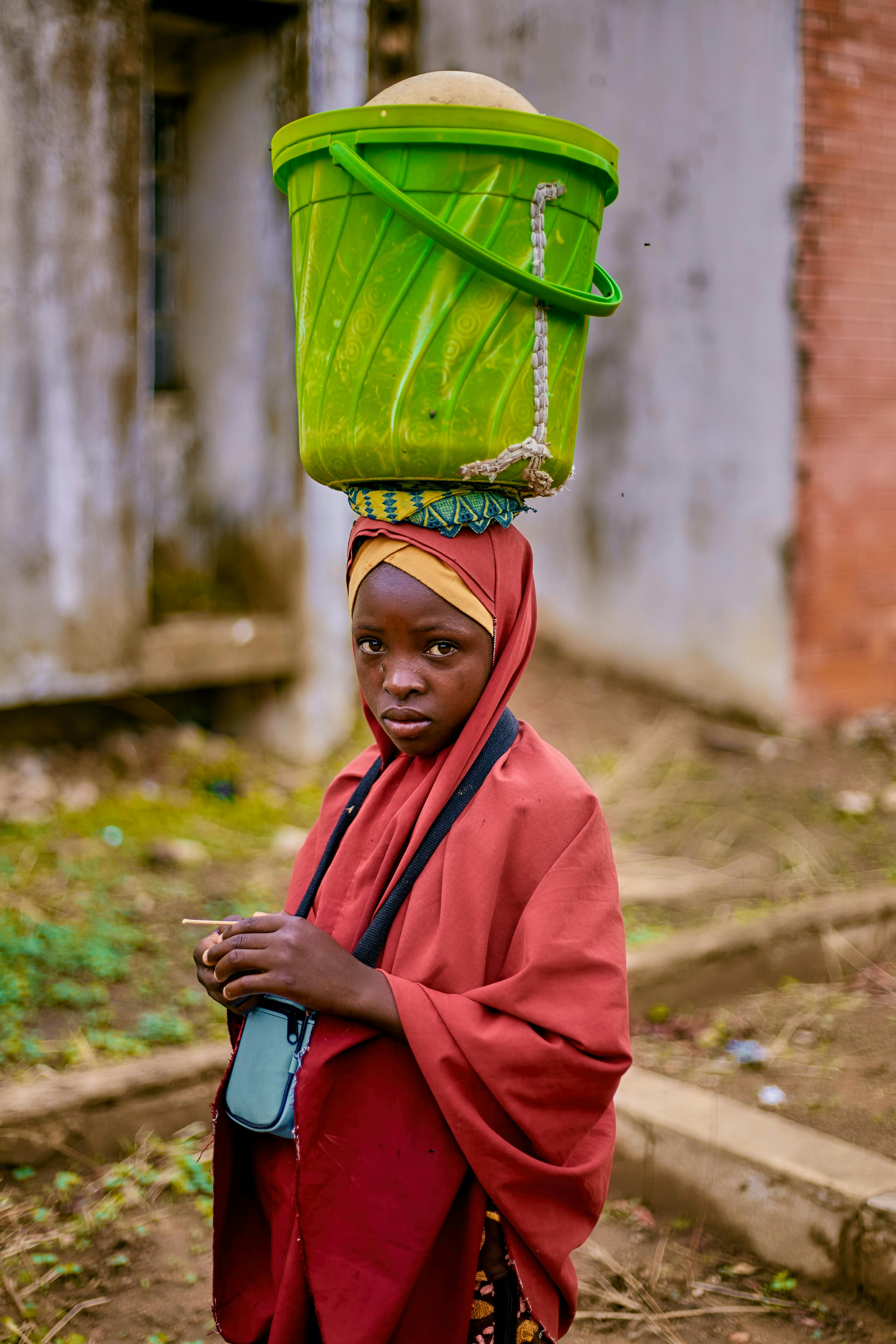 Young Girl Balancing Green Bucket Outdoors · Free Stock Photo