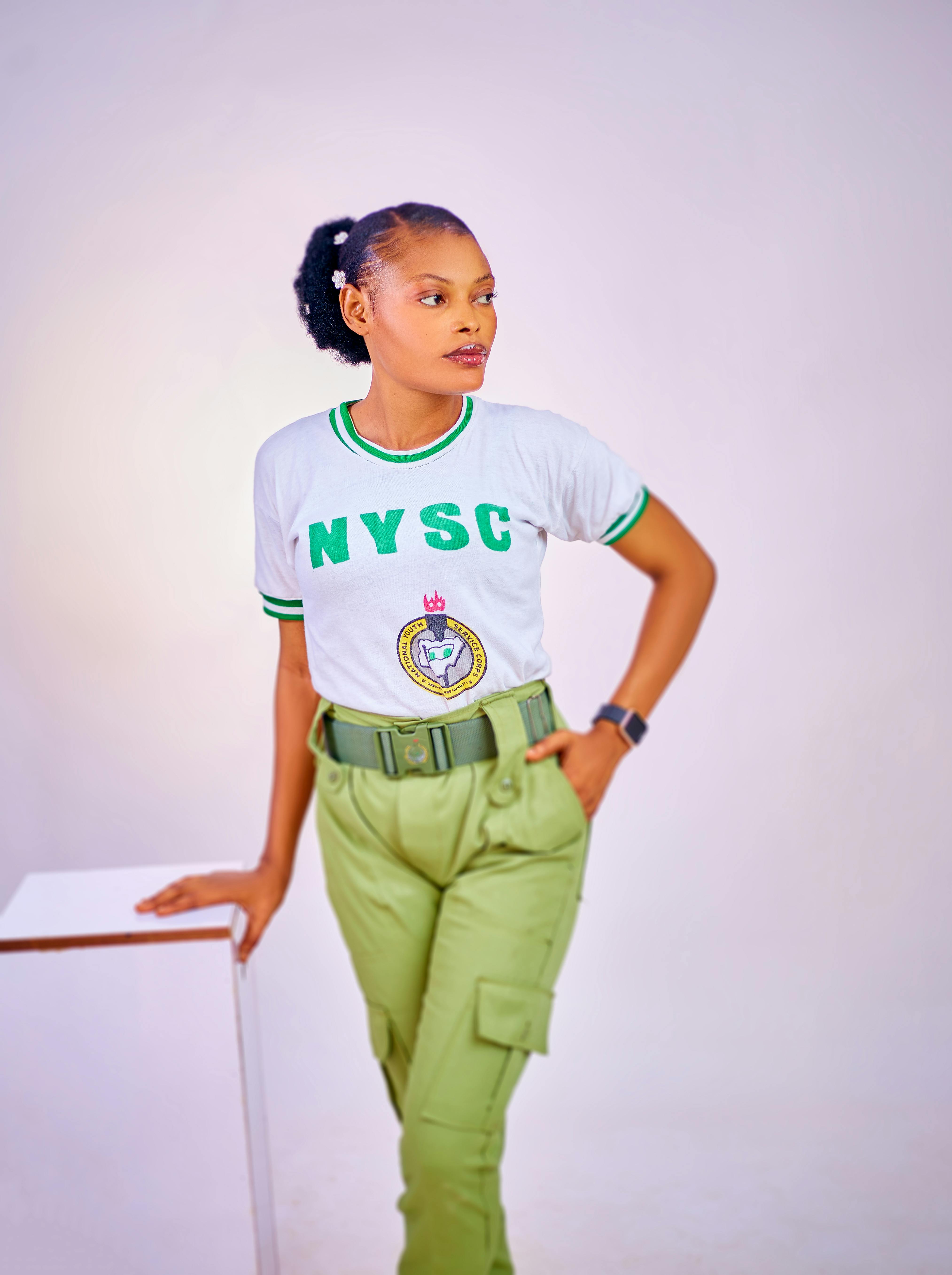 Free Woman in NYSC attire posing confidently against a plain backdrop ...