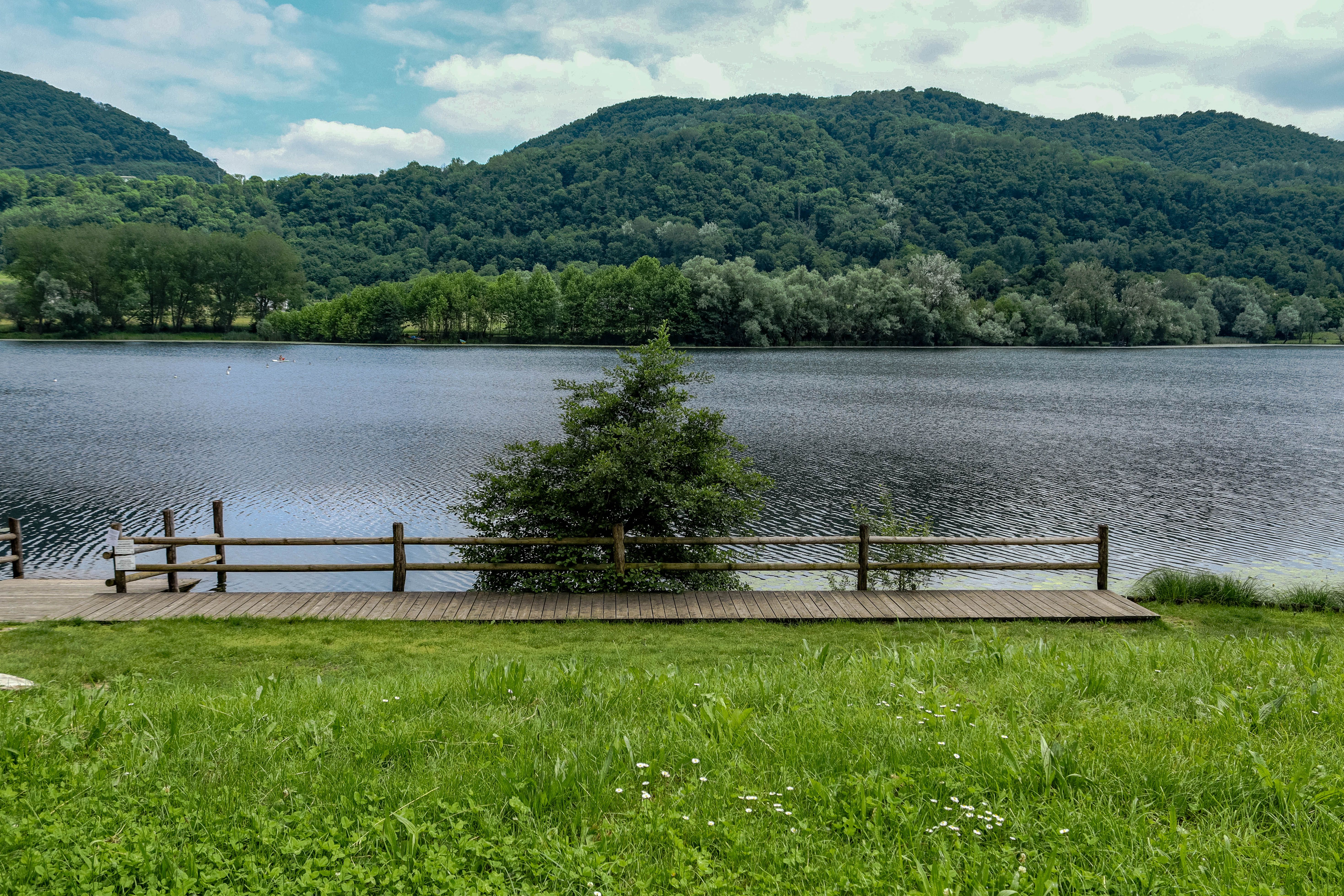 Scenic Lakeside with Lush Green Hills and Wooden Path · Free Stock Photo